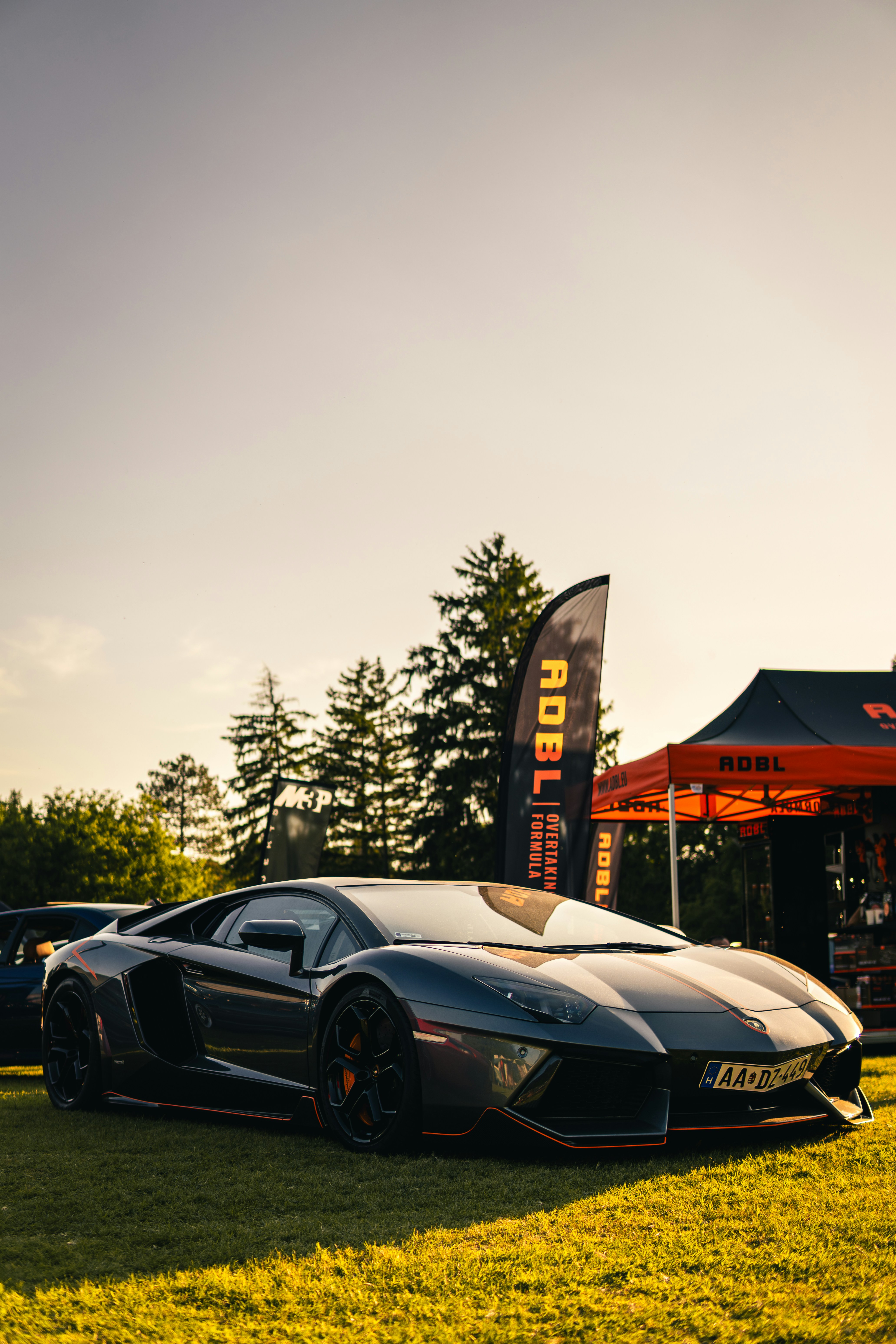 Sunset Velocity: A Low-Slung Gray Supercar at a Parkside Car Show