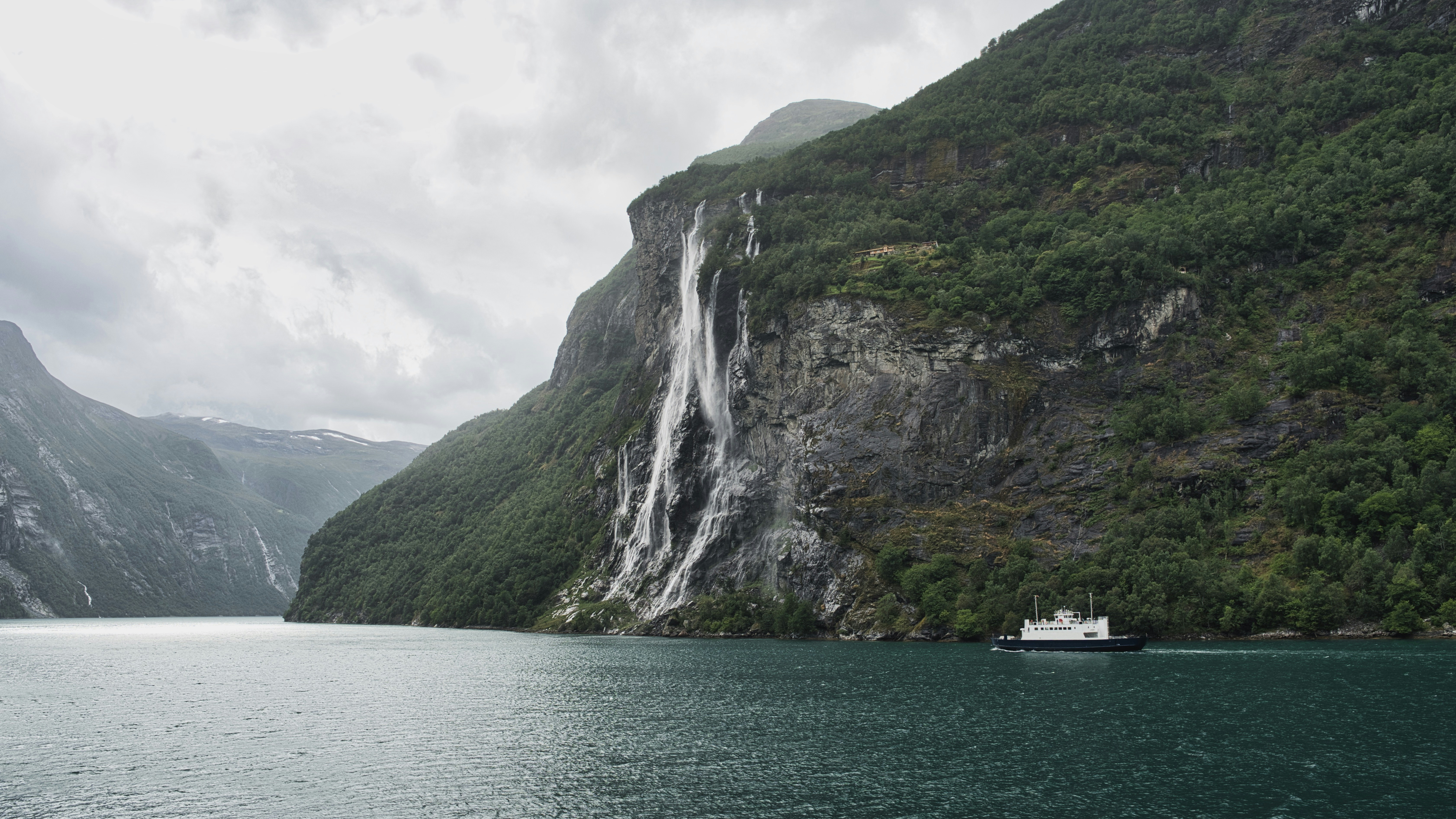 Waterfall cascading down a steep, green mountainside into a fjord.