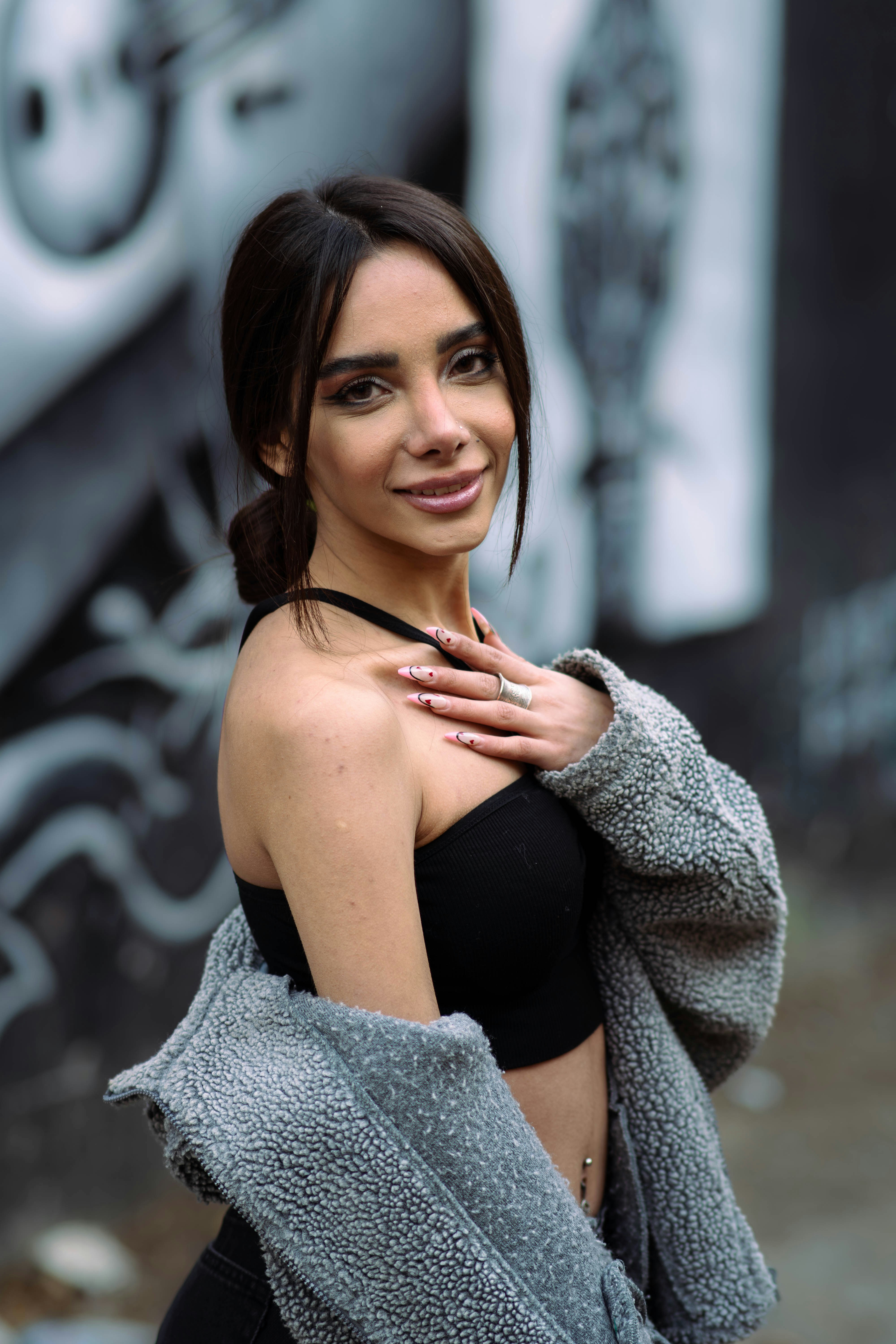 A young woman with dark hair smiles against graffiti