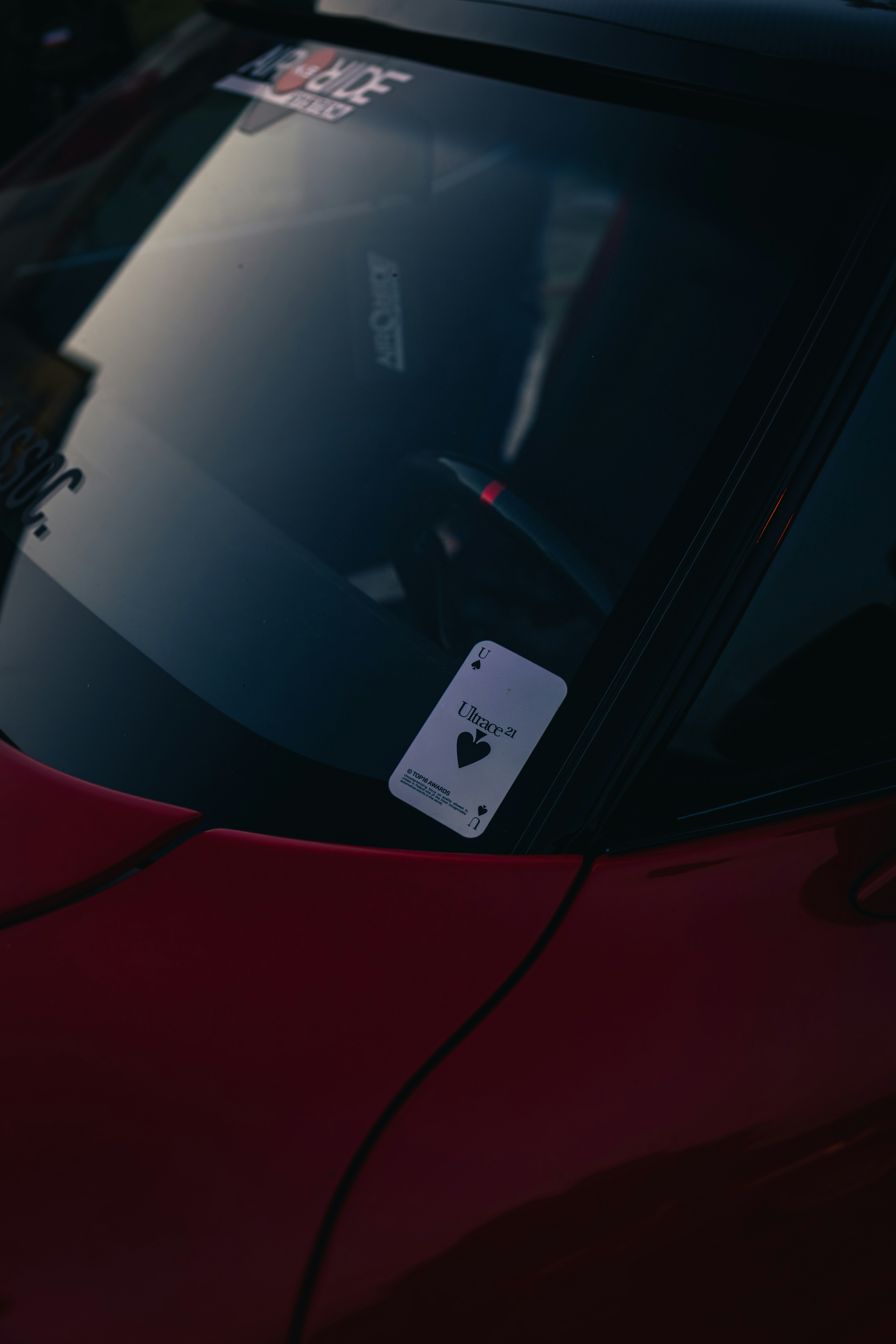 Card on Glass: A White Playing Card Quietly Anchors a Red Car at Dusk