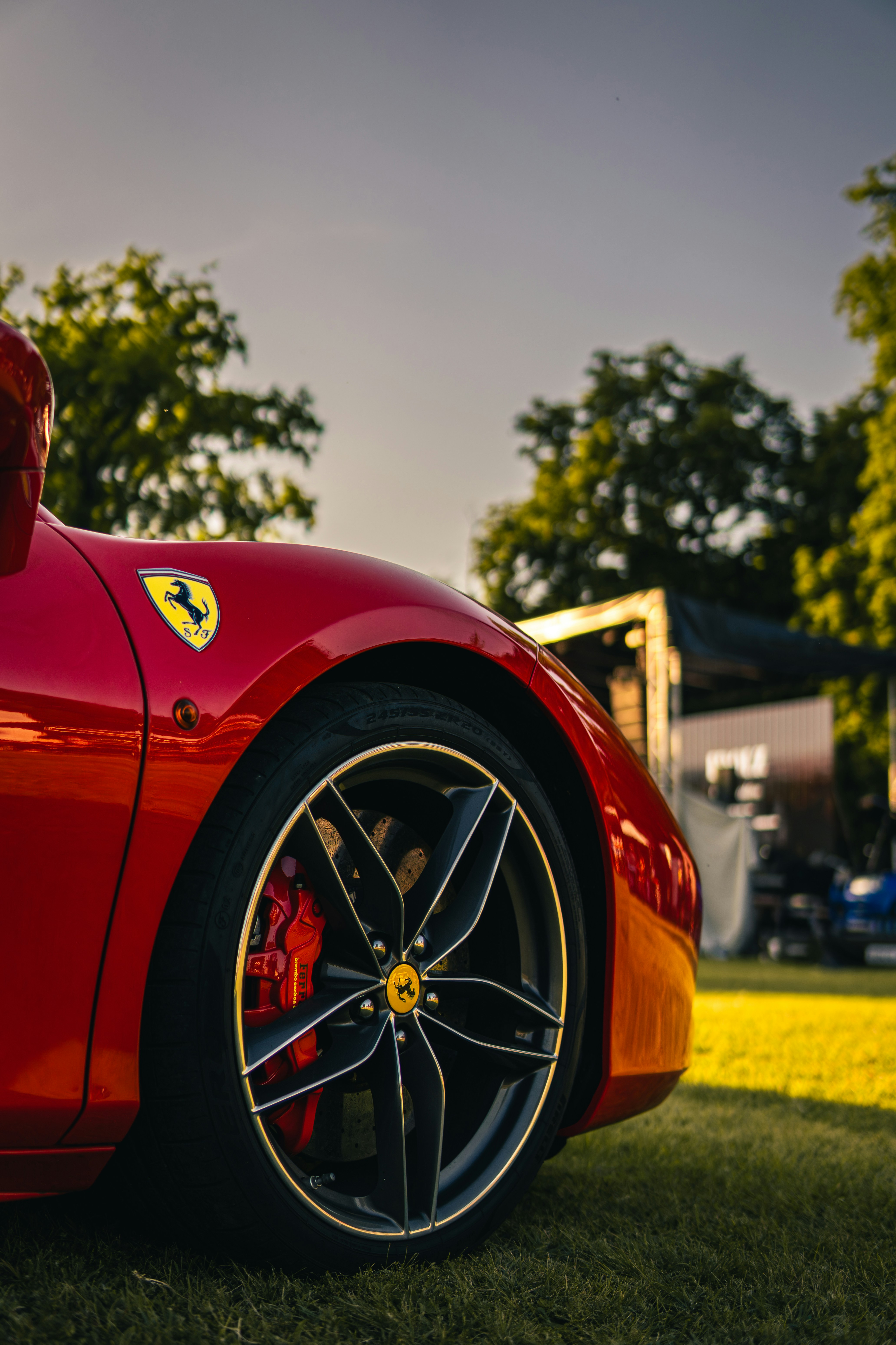 Close-up of a Ferrari's wheel and logo, showcasing the exquisite design and craftsmanship against a lush green backdrop.