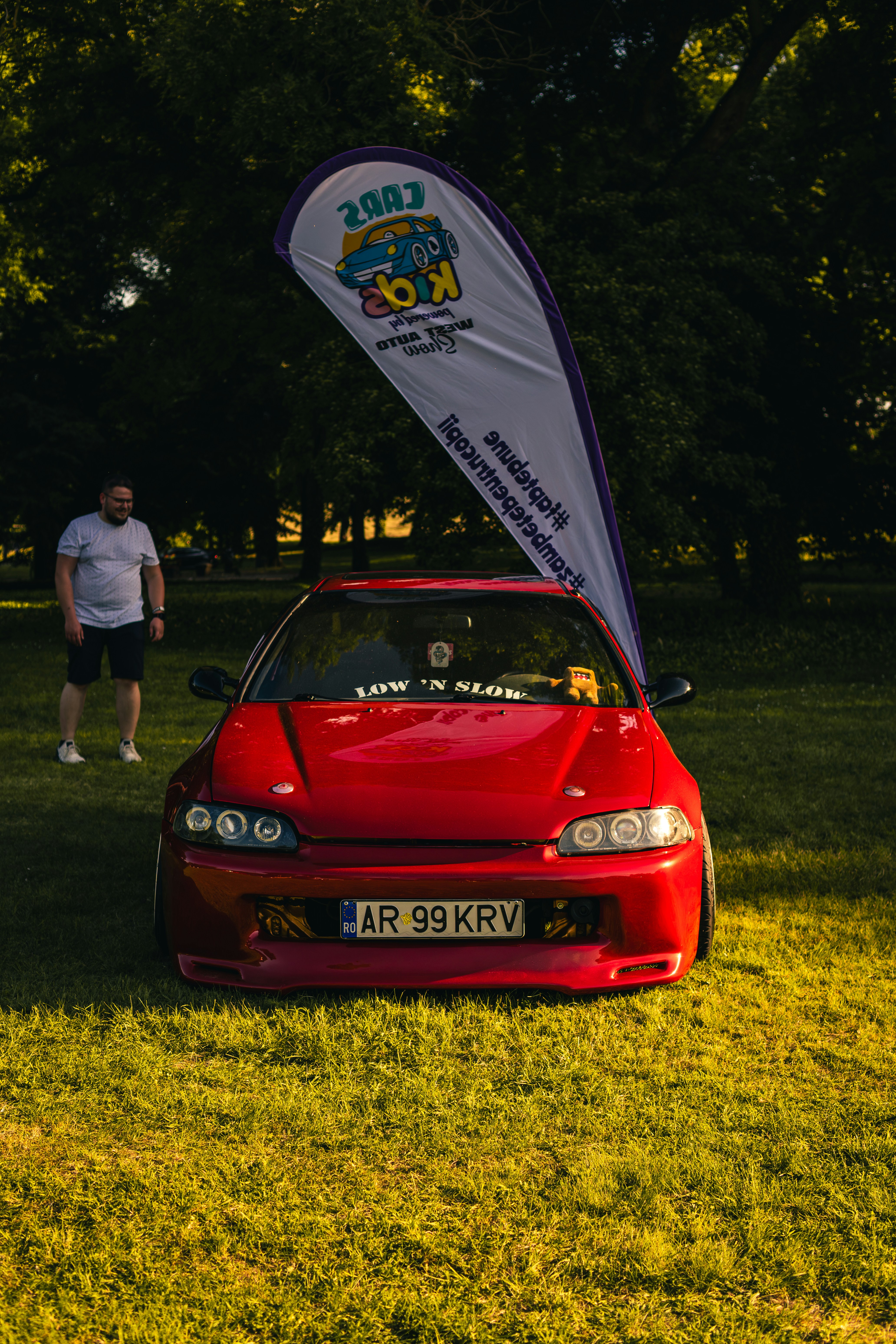 Crimson Coupe Beneath a Park Banner: A Quiet Showroom Moment