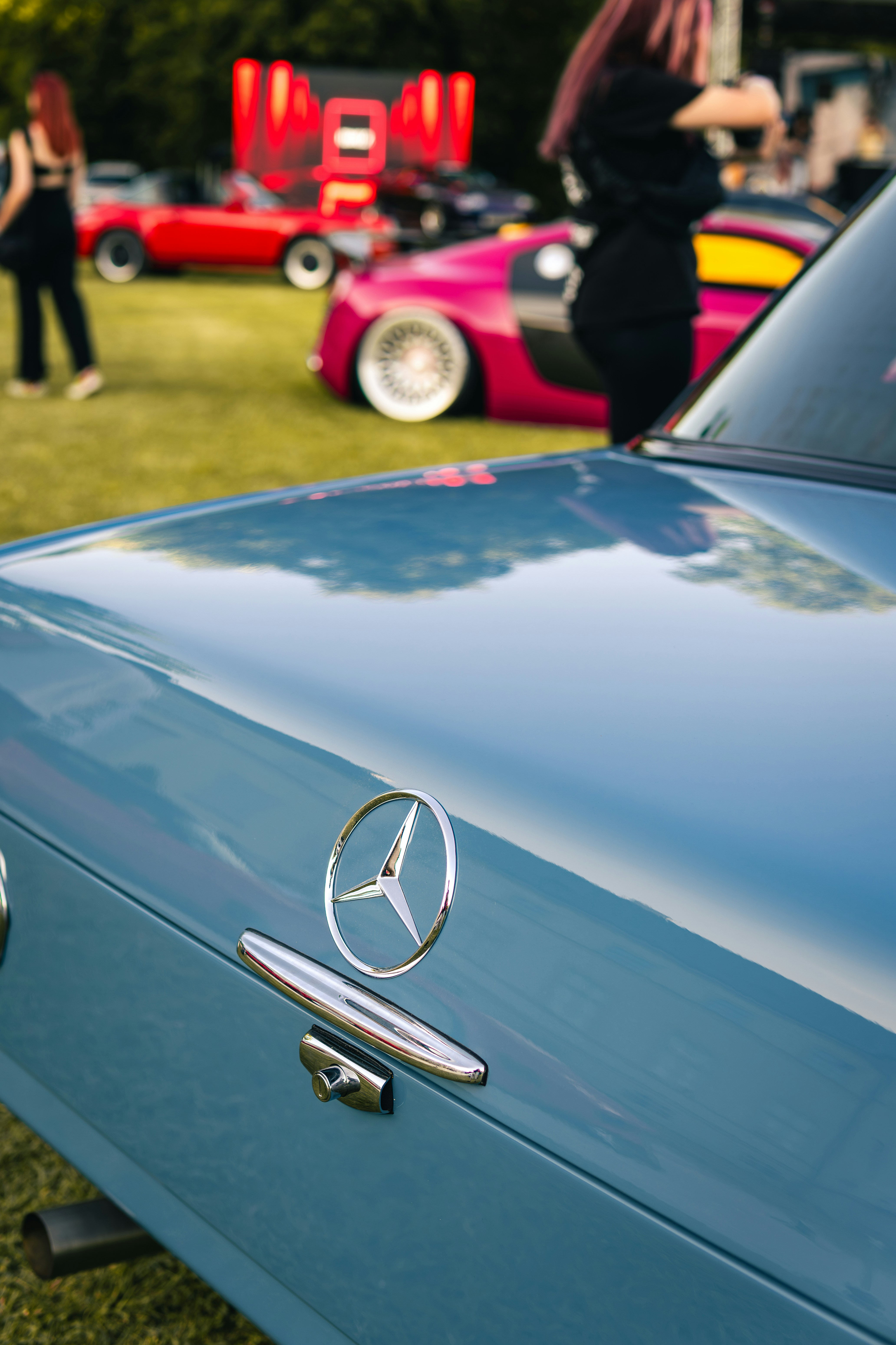Cerulean Mercedes Emblem Anchors a Classic Hood Amid a Soft Car-Show Blur