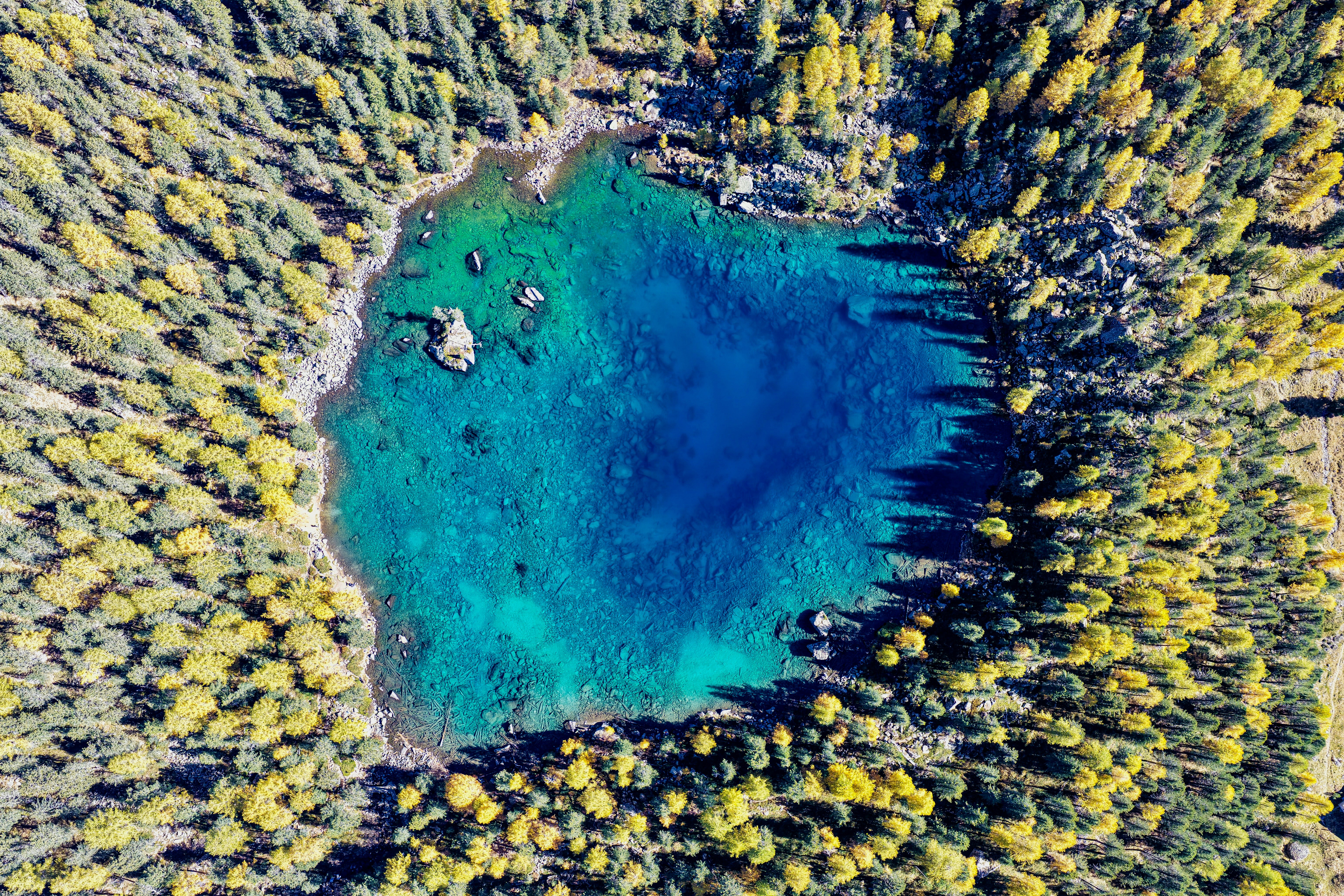 A pristine, circular lake surrounded by vibrant autumn foliage, showcasing a striking contrast between deep blue water and golden leaves. The scene captures a serene natural landscape.