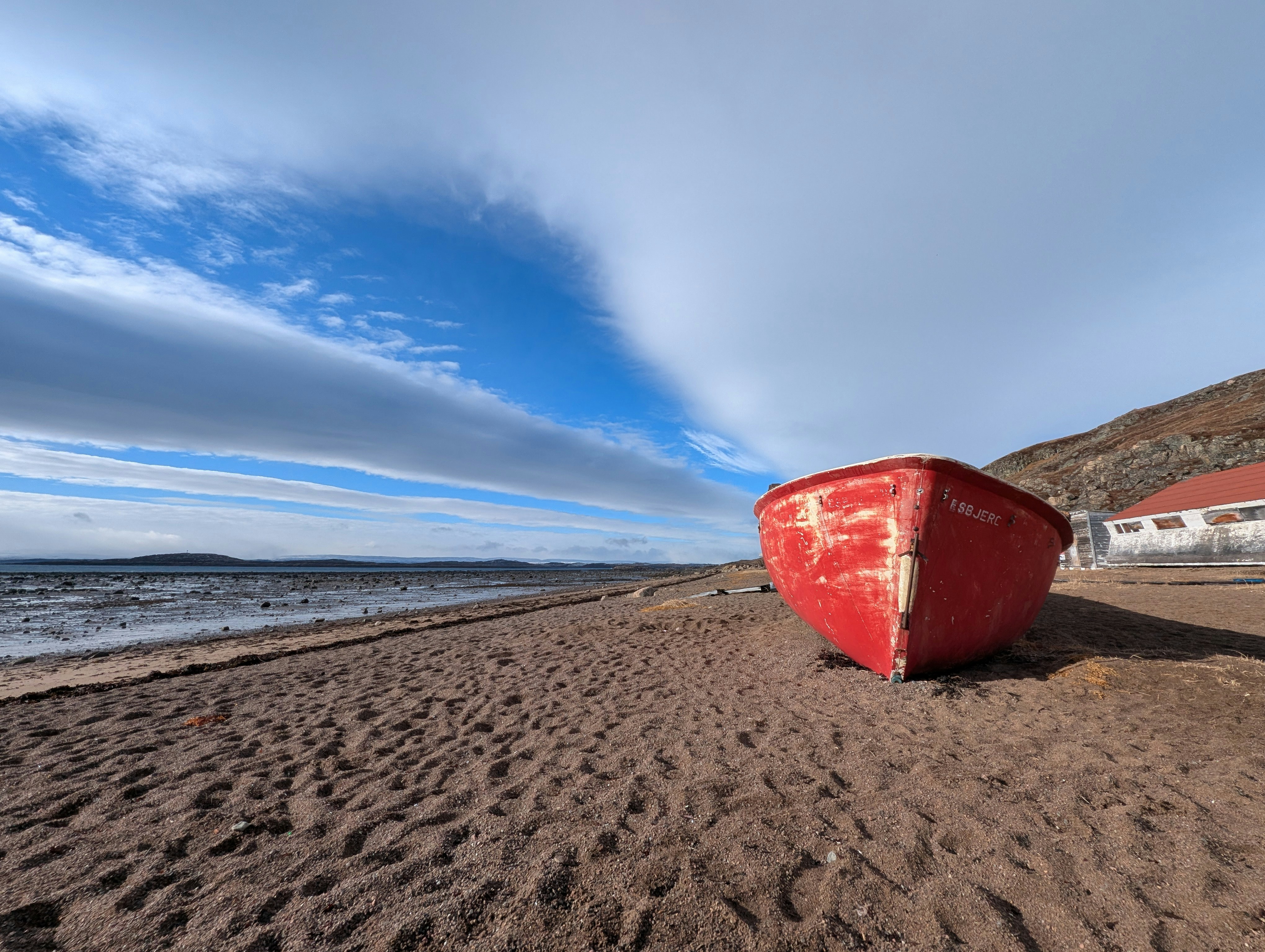 Red rowboat resting on a sandy beach under clouds