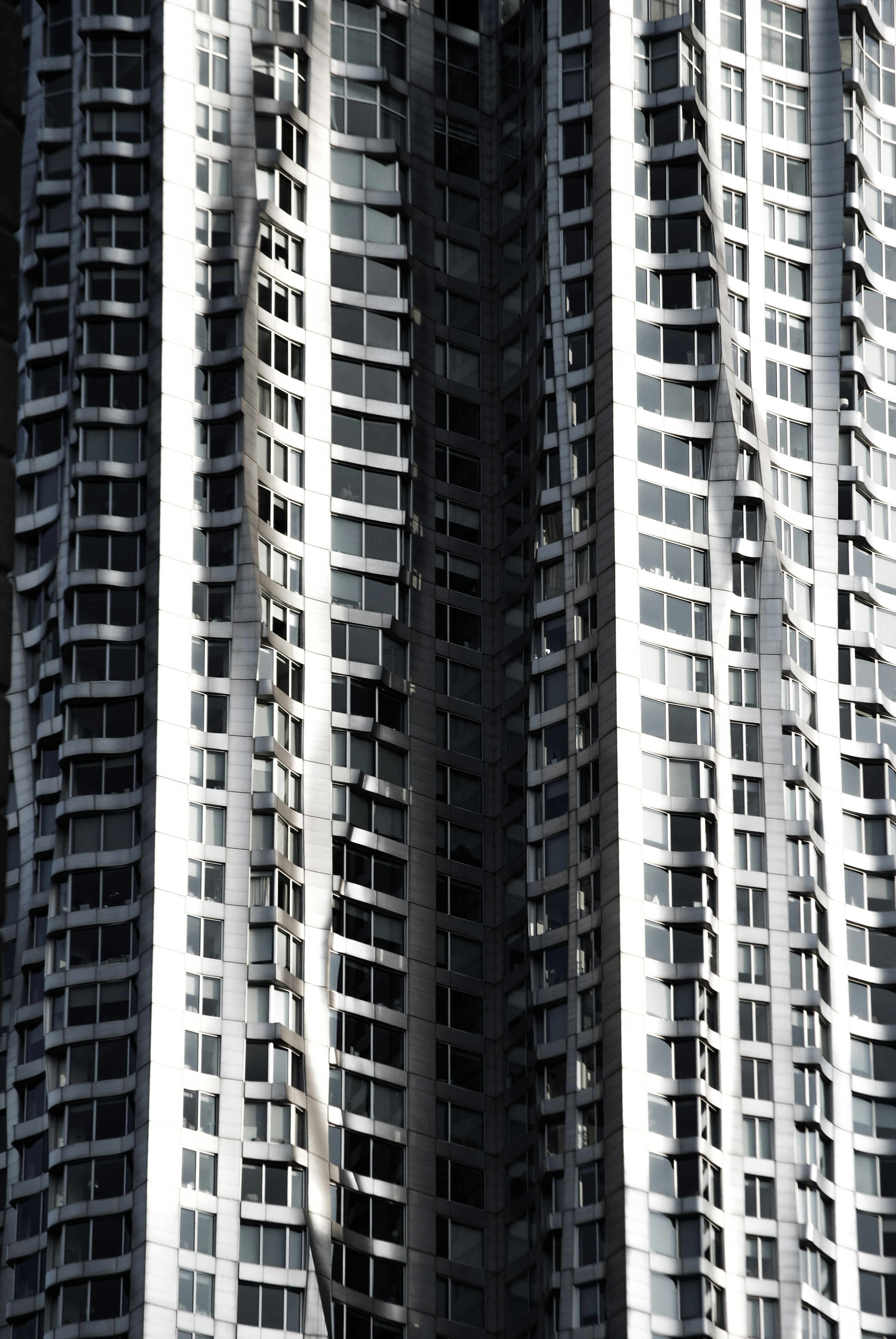 Curved glass facade of a modern skyscraper reflecting light and shadows in intricate patterns.