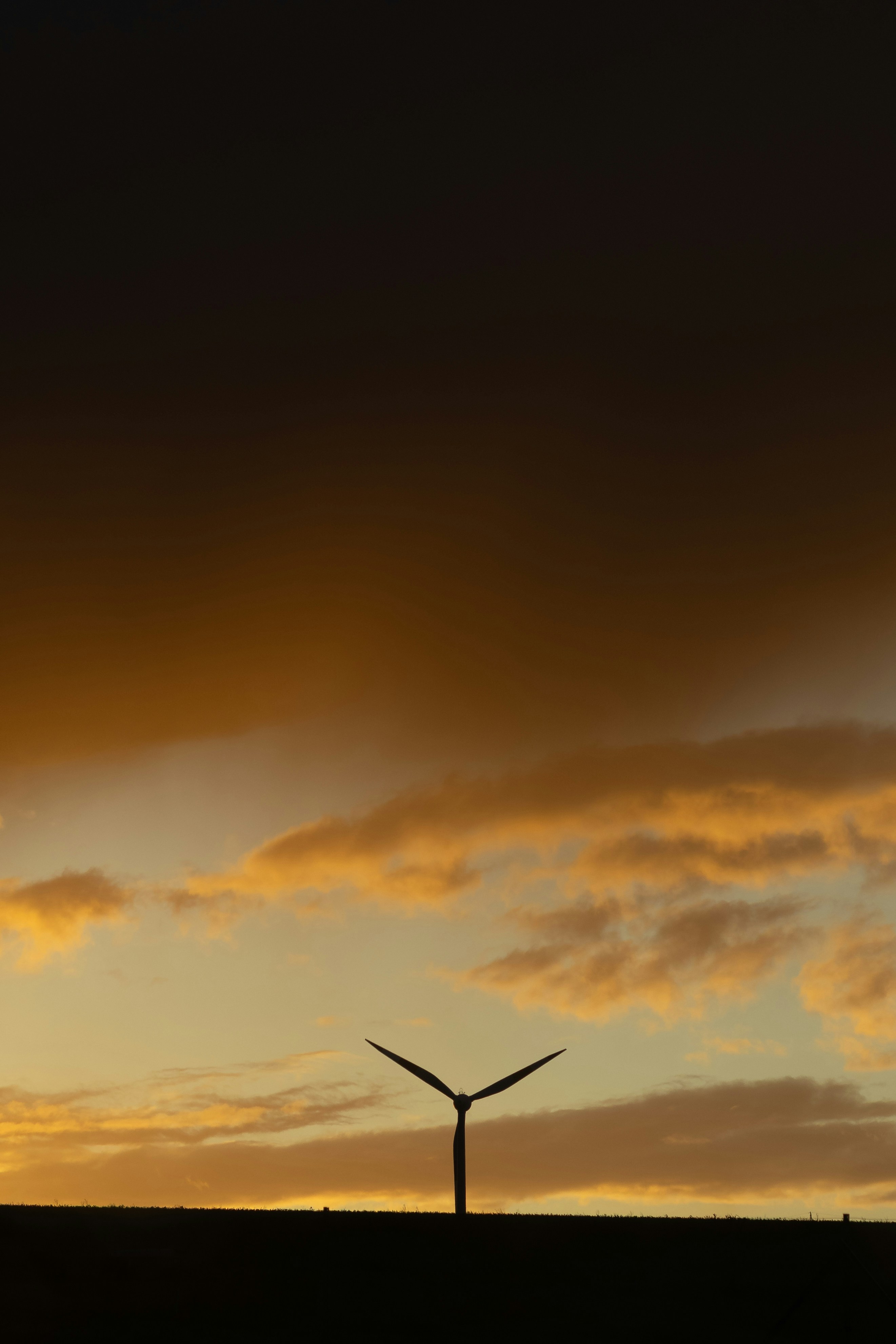 Wind turbine silhouetted against a cloudy sunset sky at sunset