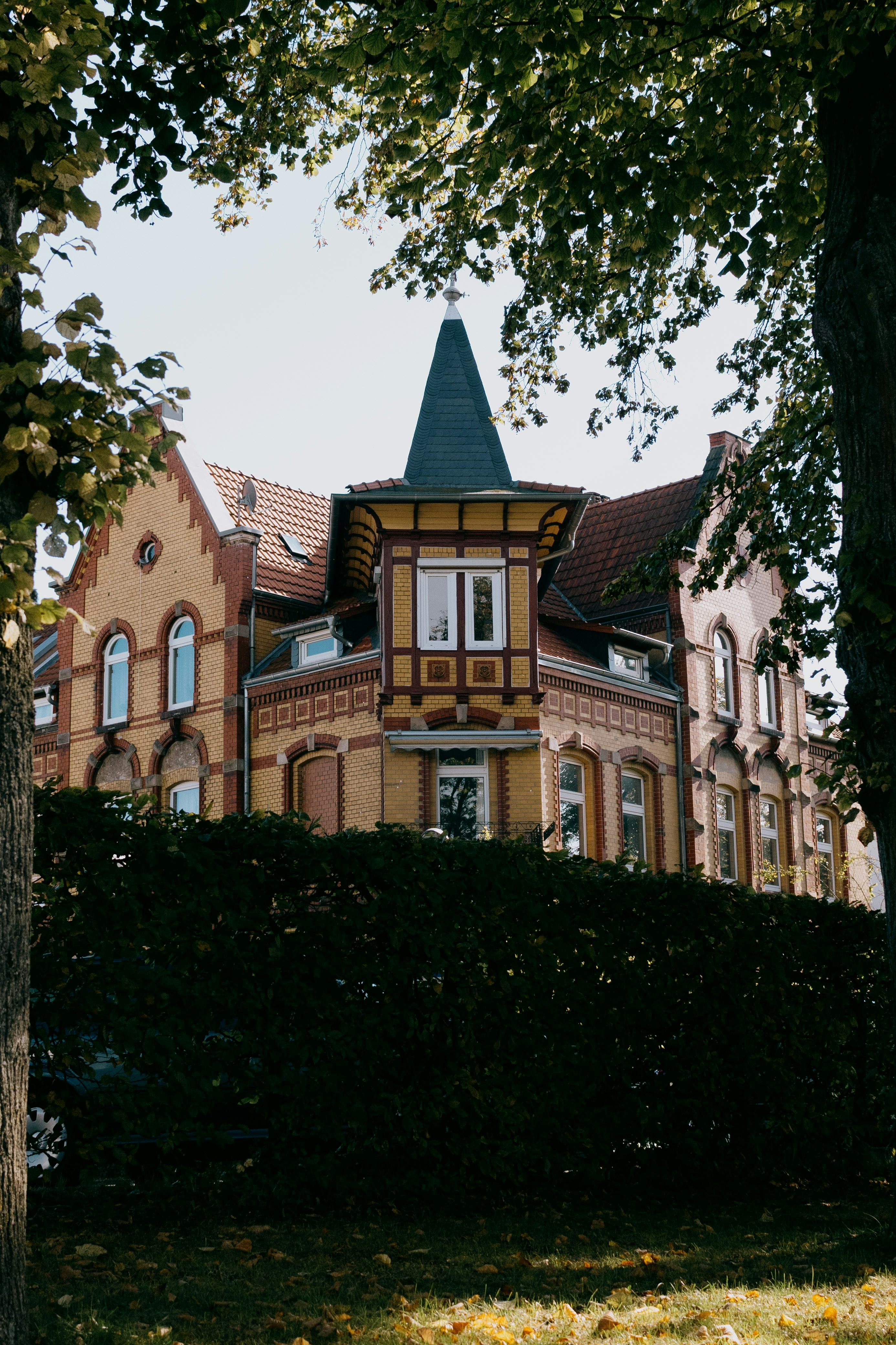 Yellow brick house with green hedge and trees