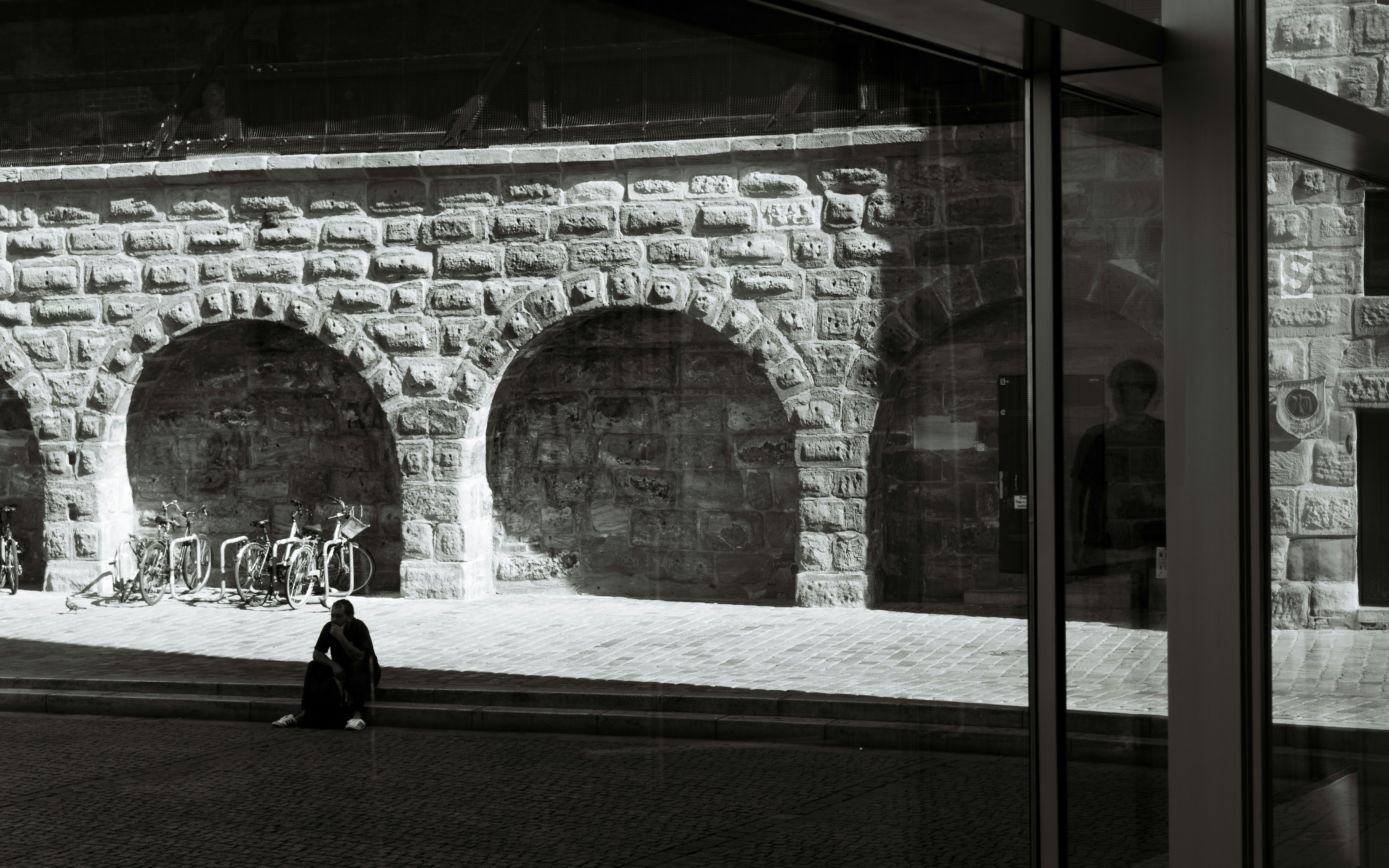 Person sitting near stone arches in black and white.