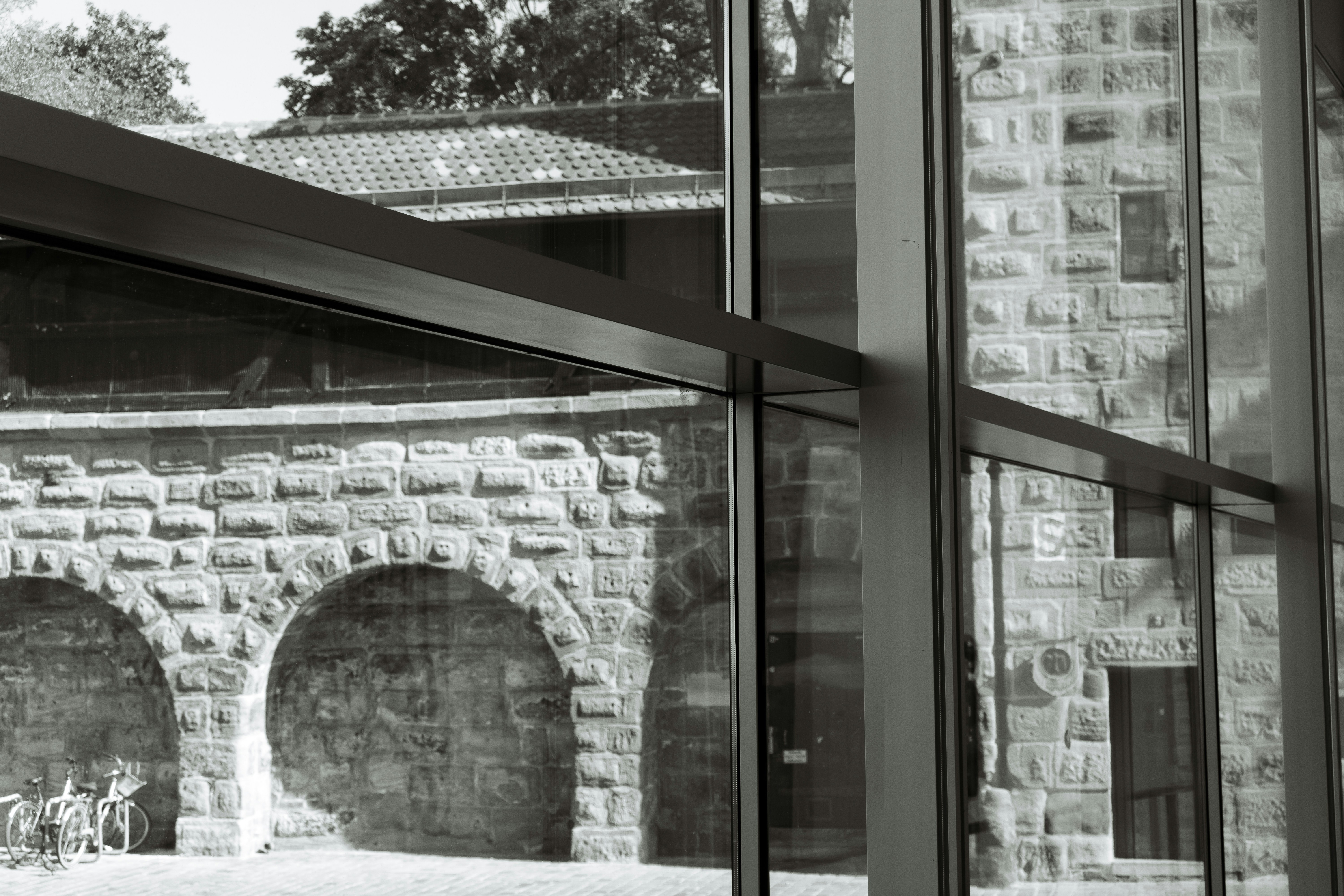 Historic stone arches reflected in modern glass architecture, showcasing a blend of old and new design elements.
