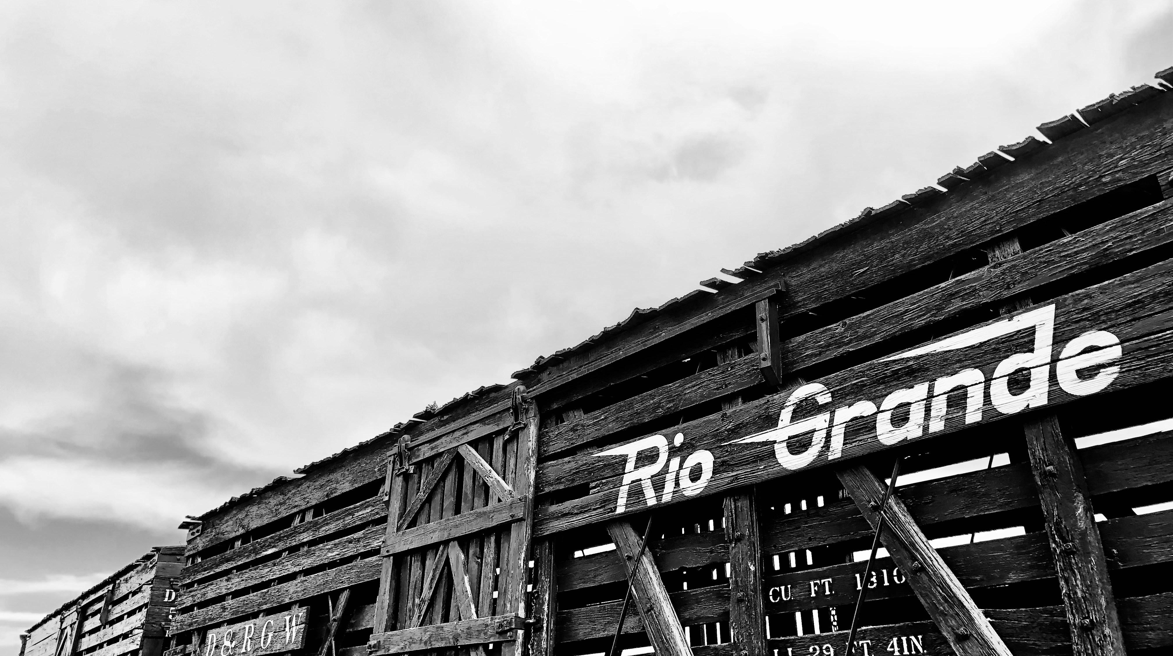 Weathered wooden structure adorned with the name 'Rio Grande' in bold lettering, set against a dramatic sky. The monochrome tones enhance the rustic charm.