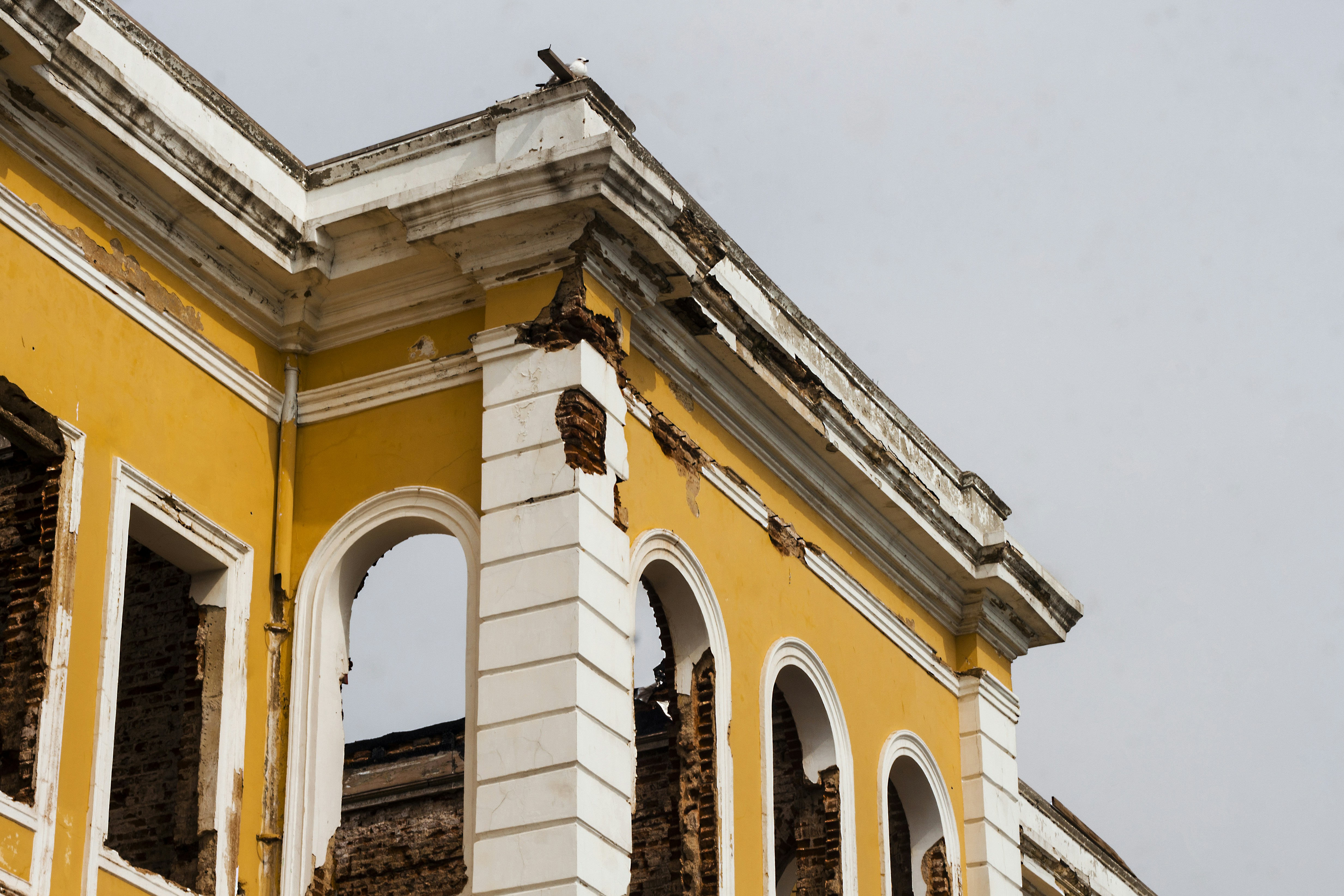Yellow building with arched windows and damaged facade.