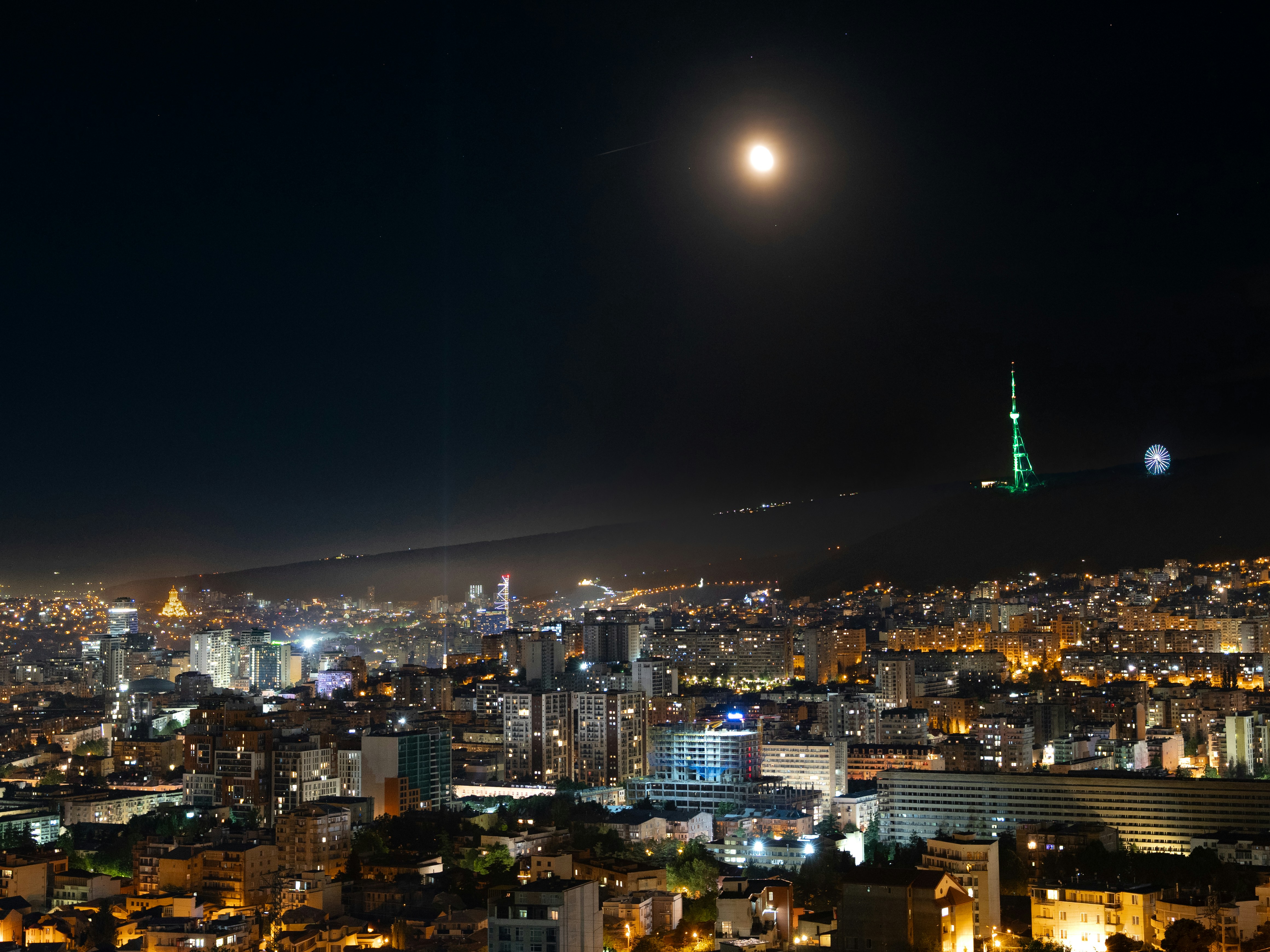 Cityscape at night with illuminated buildings and moon.