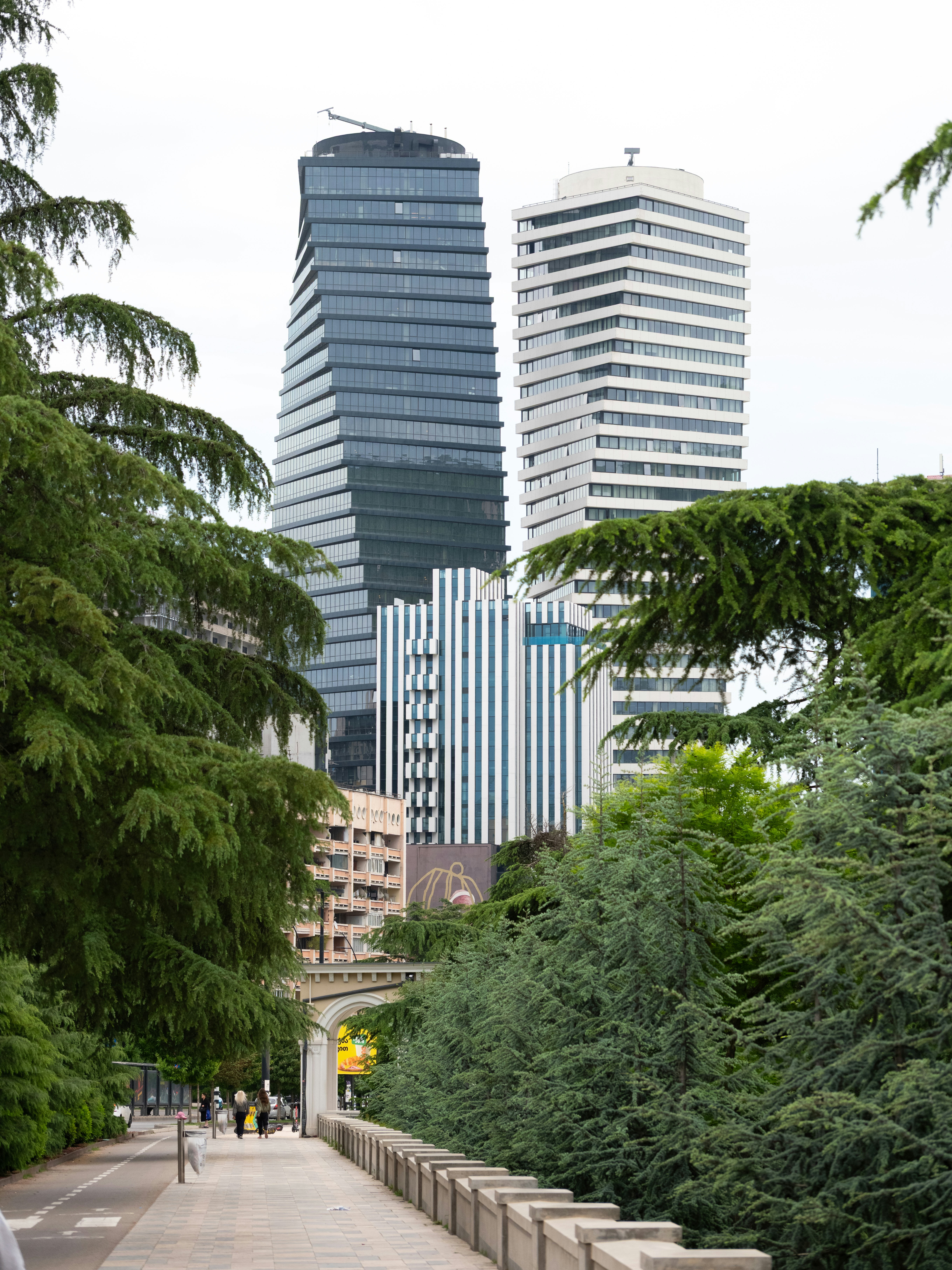Modern skyscrapers rise behind lush green trees.