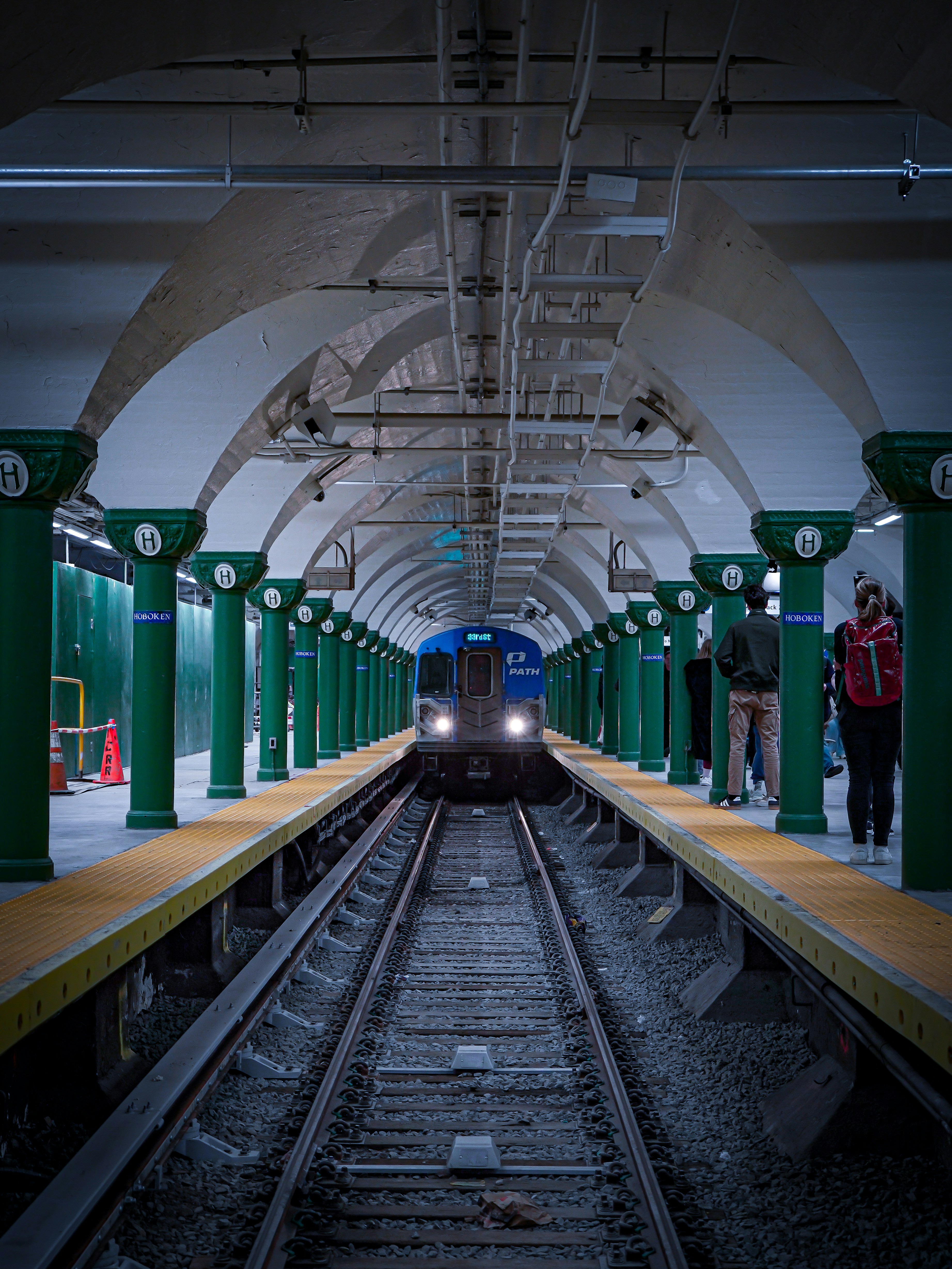 Subway train approaching a platform in a historic underground station, with passengers waiting and architectural details highlighted. 