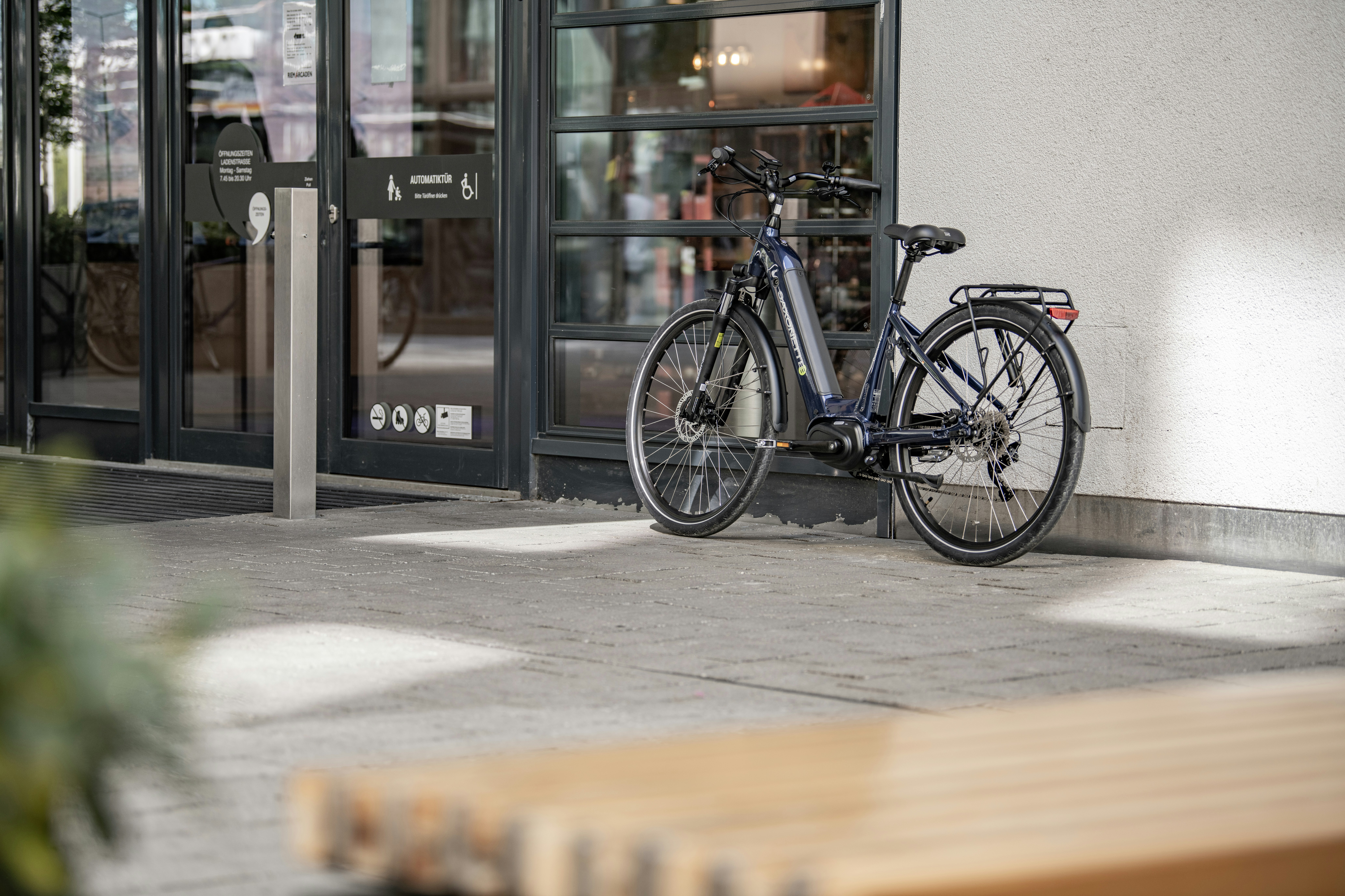 A sleek electric bicycle parked beside a modern building entrance, showcasing urban mobility solutions. The scene highlights the blend of technology and architecture.