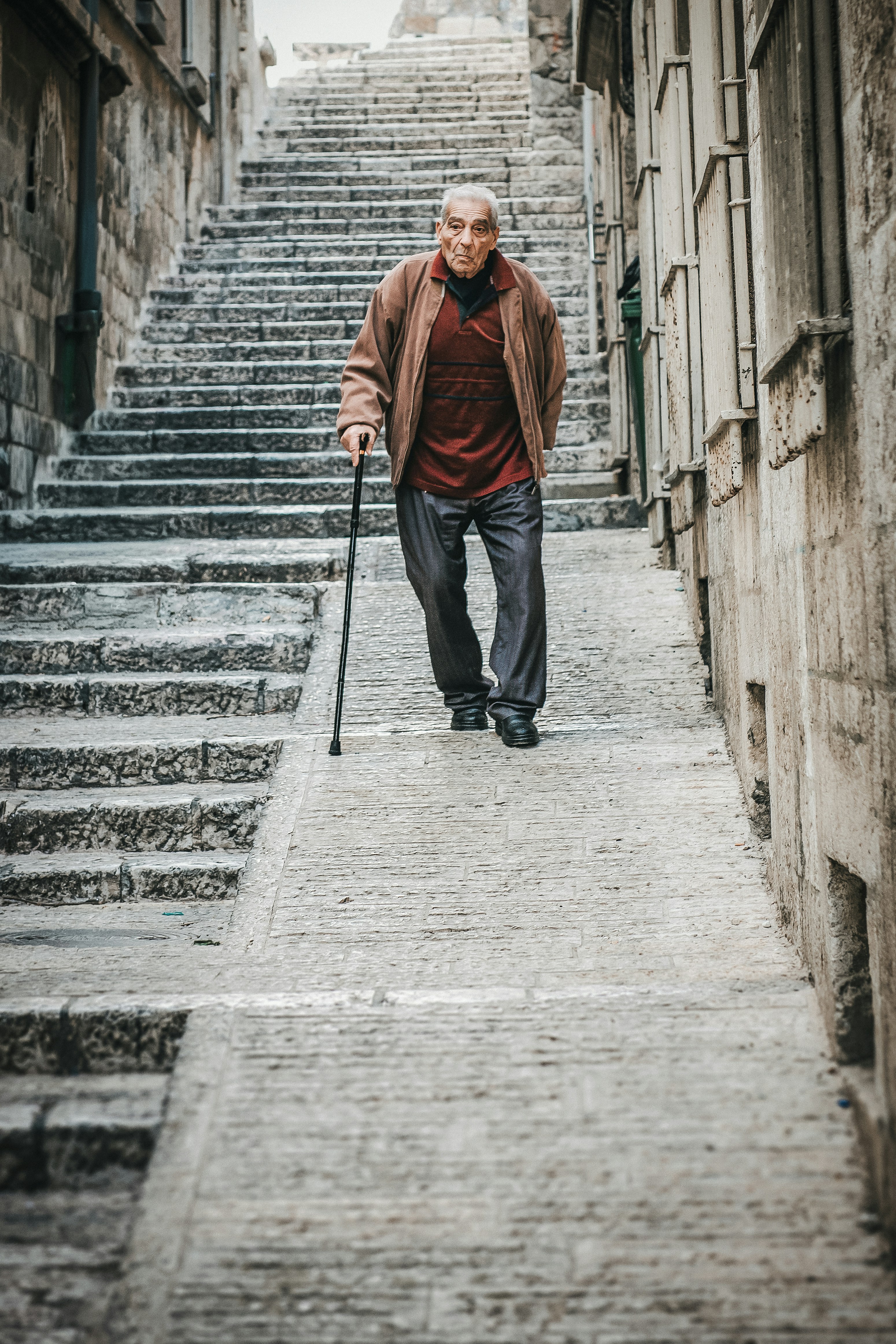 Elderly man navigating steep cobblestone stairs with a cane, embodying determination and strength.