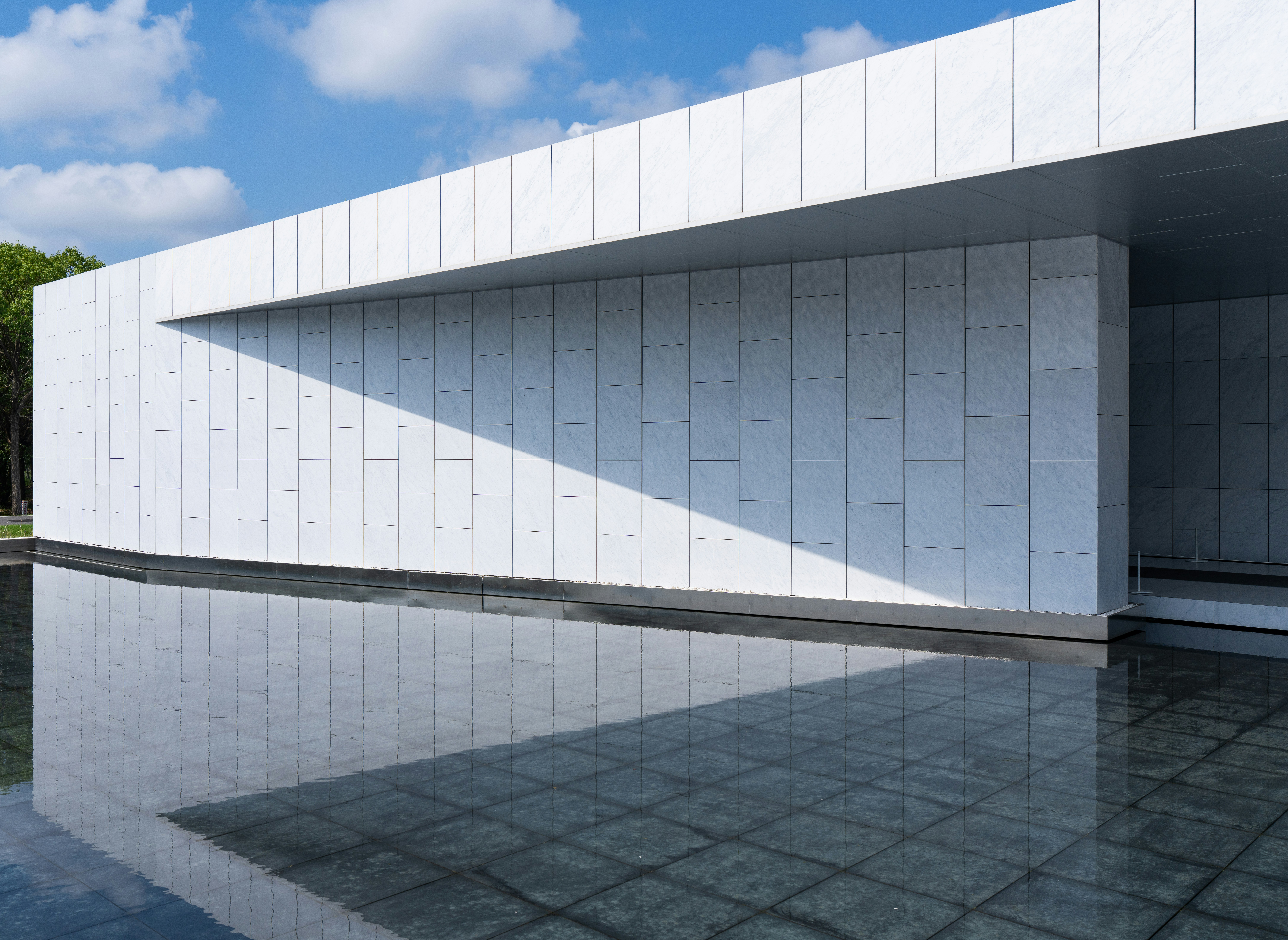 Minimalist architecture featuring a sleek white facade and a reflective pool, showcasing the interplay of light and shadow.