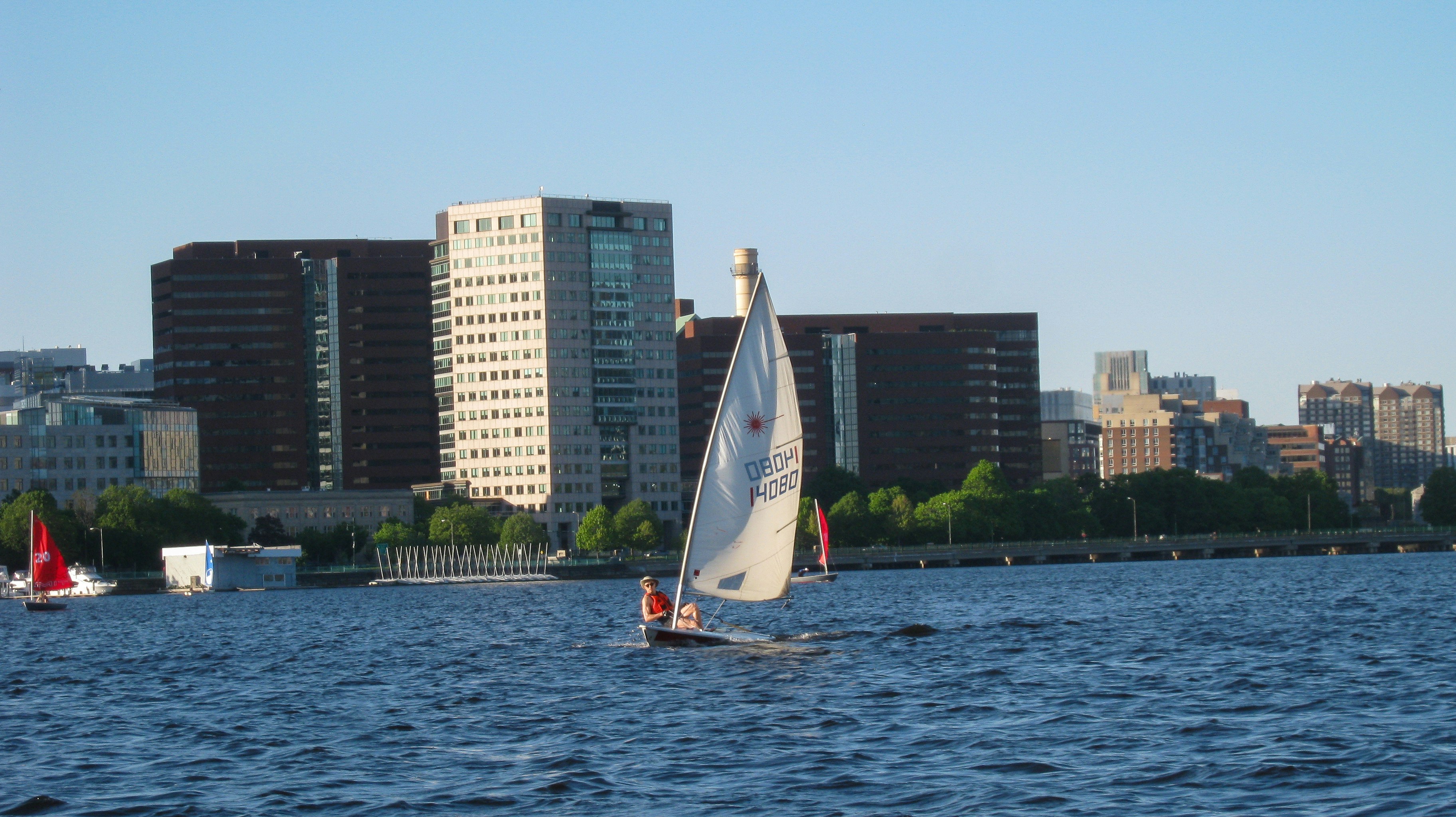 Man sailing on the Charles River - Cambridge, MA | Sailboat on water with city buildings background
