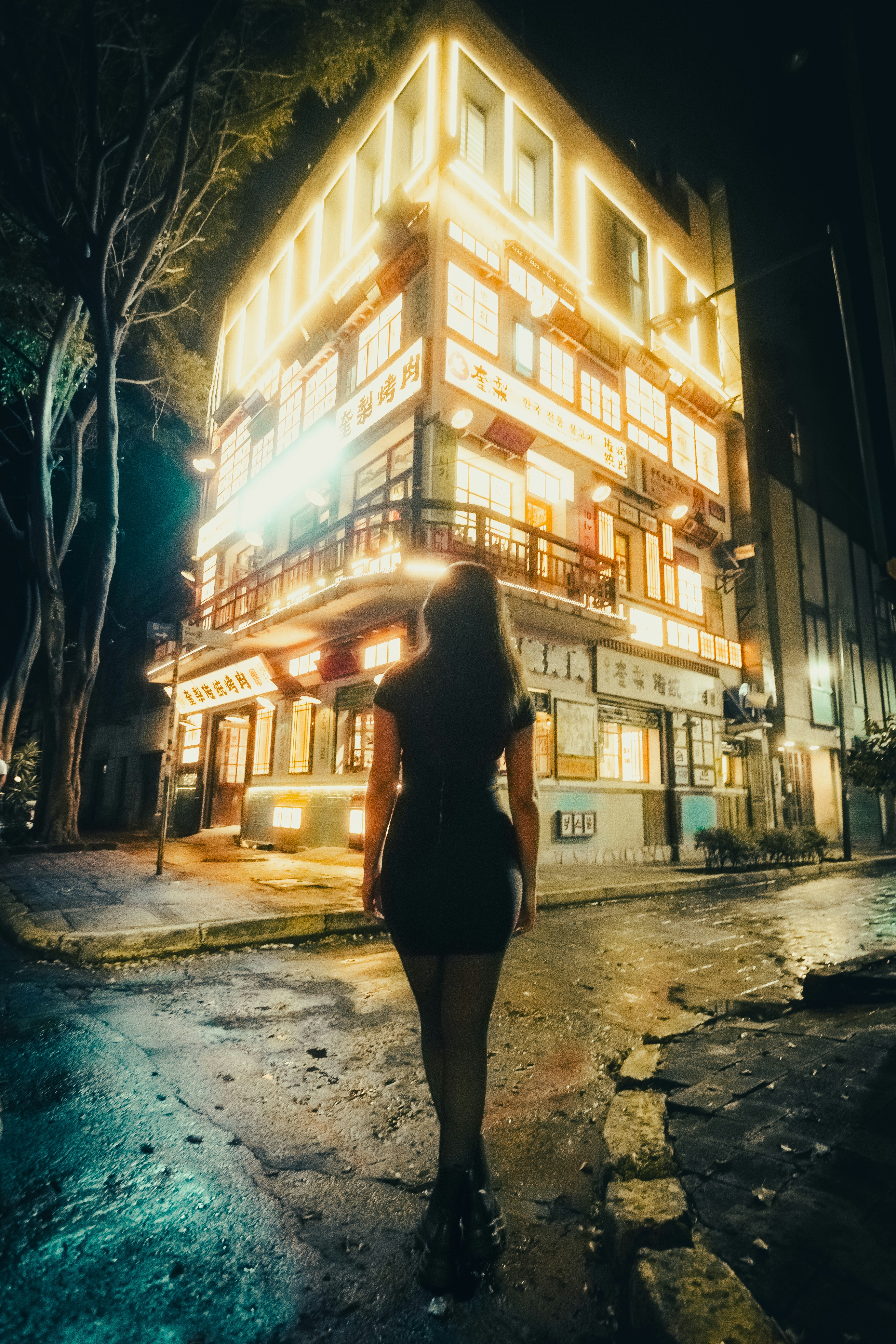 Woman walks towards brightly lit building at night