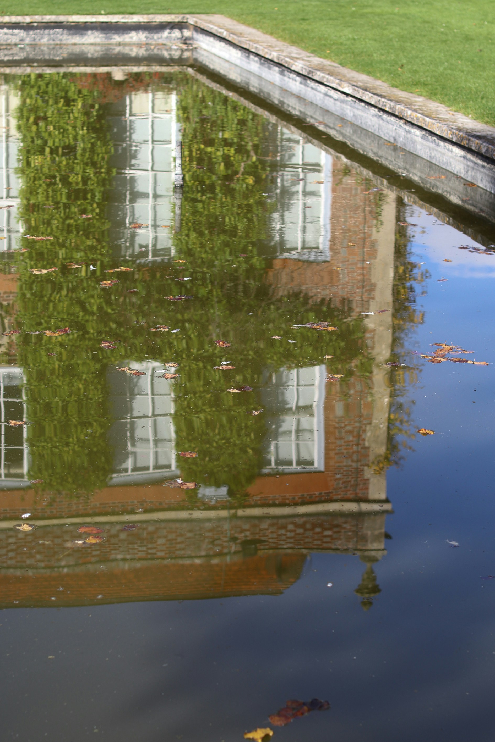 A serene reflection of a brick building adorned with greenery in a calm pond, capturing the harmony between nature and architecture.
