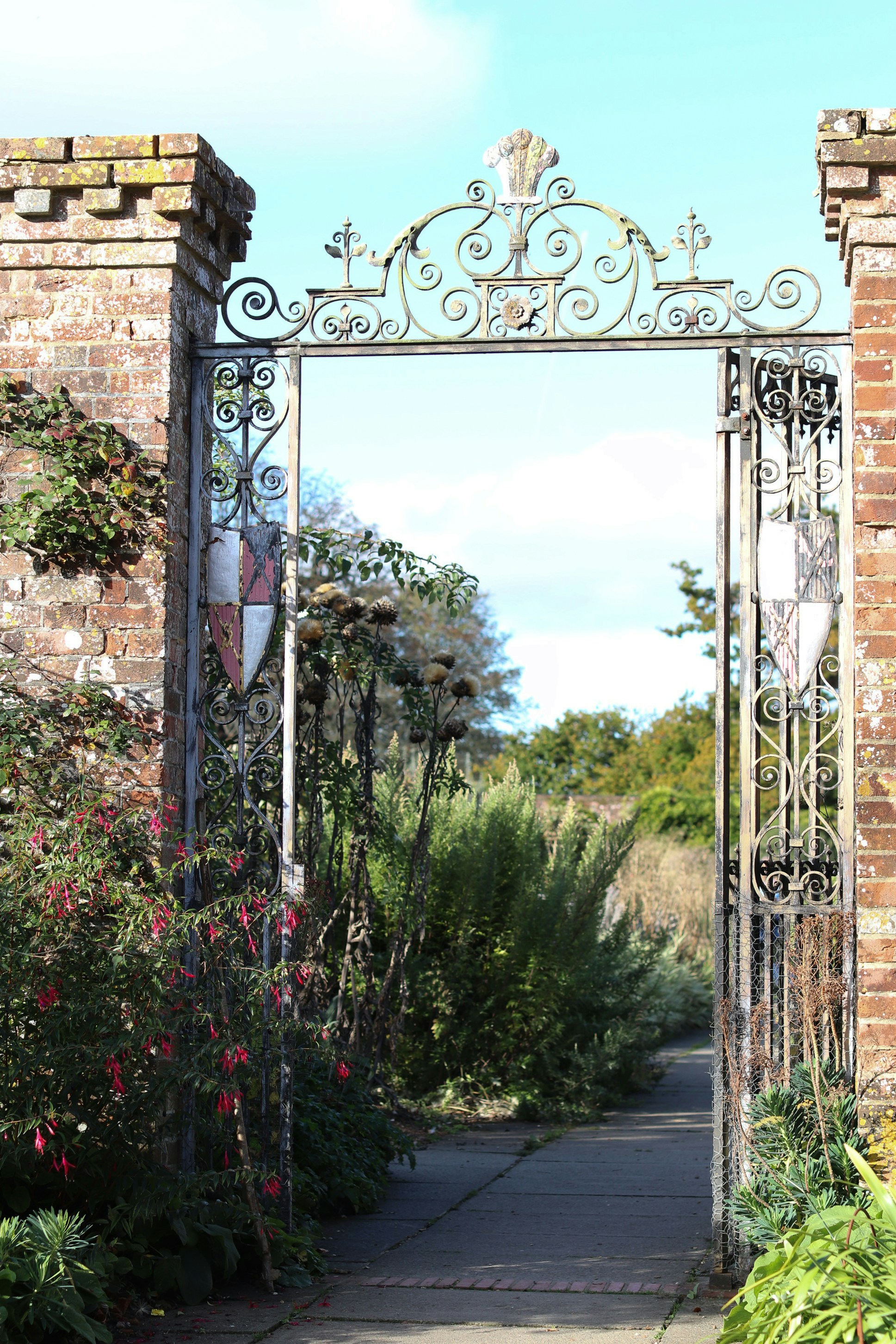 Intricately designed wrought iron gate framed by lush greenery and vibrant flowers, inviting exploration into a serene garden space.