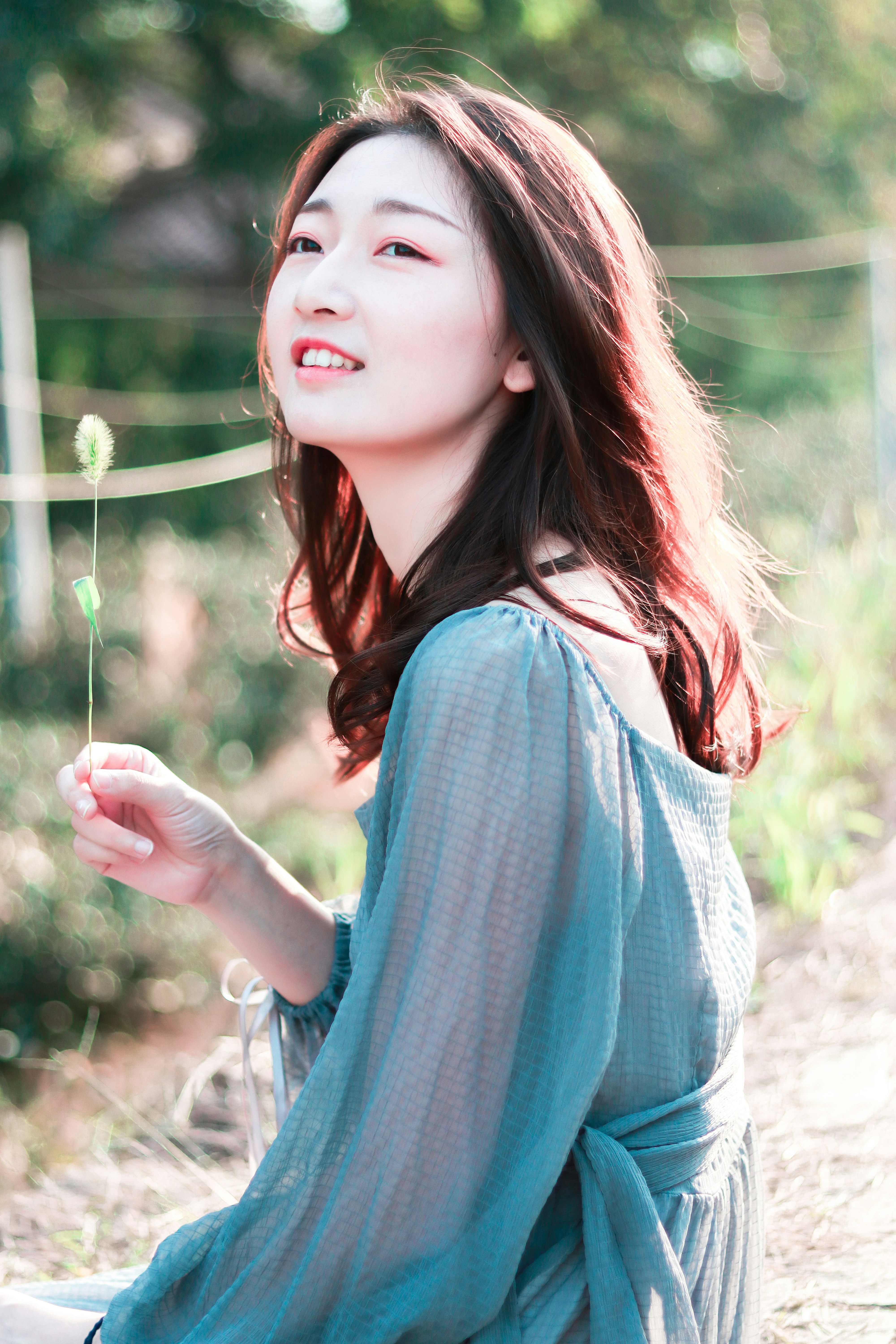 Golden sunlight shines on hair strands | Young woman holding a blade of grass outdoors