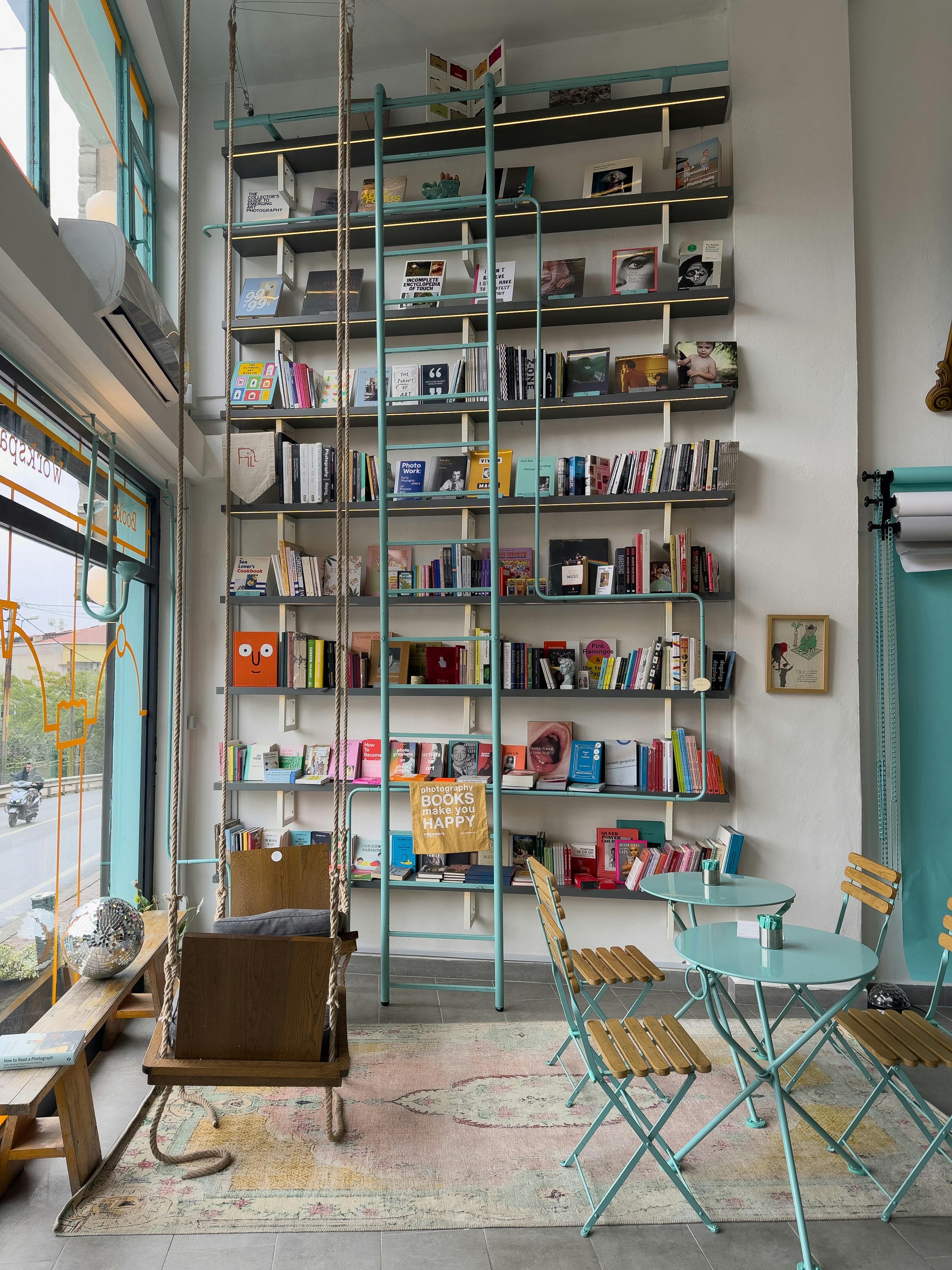 Cozy café interior featuring a vibrant bookshelf filled with colorful books, a swing chair, and a charming table set for reading. A perfect blend of comfort and creativity.