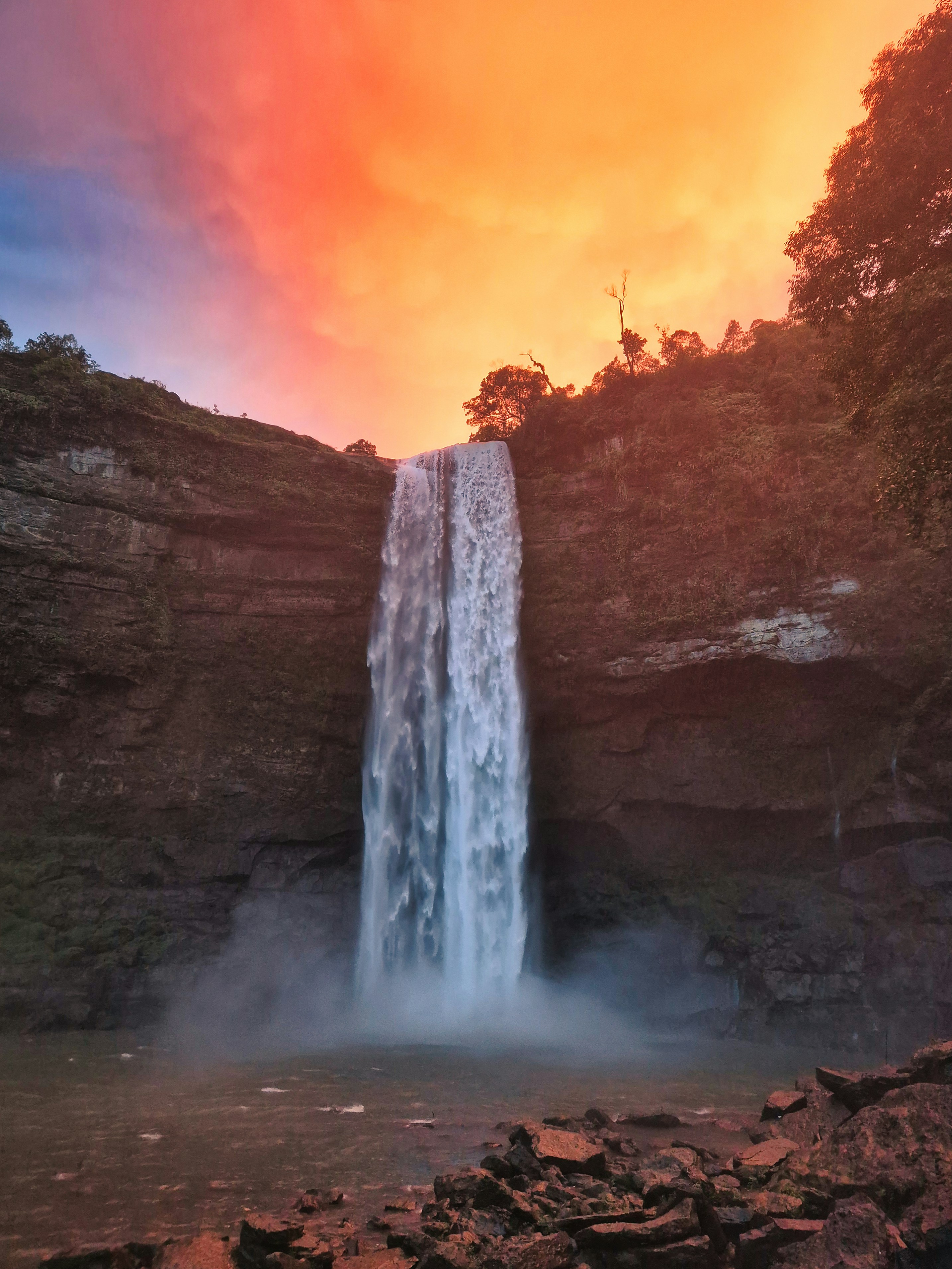 Majestic waterfall cascading down rocky cliffs at sunset.