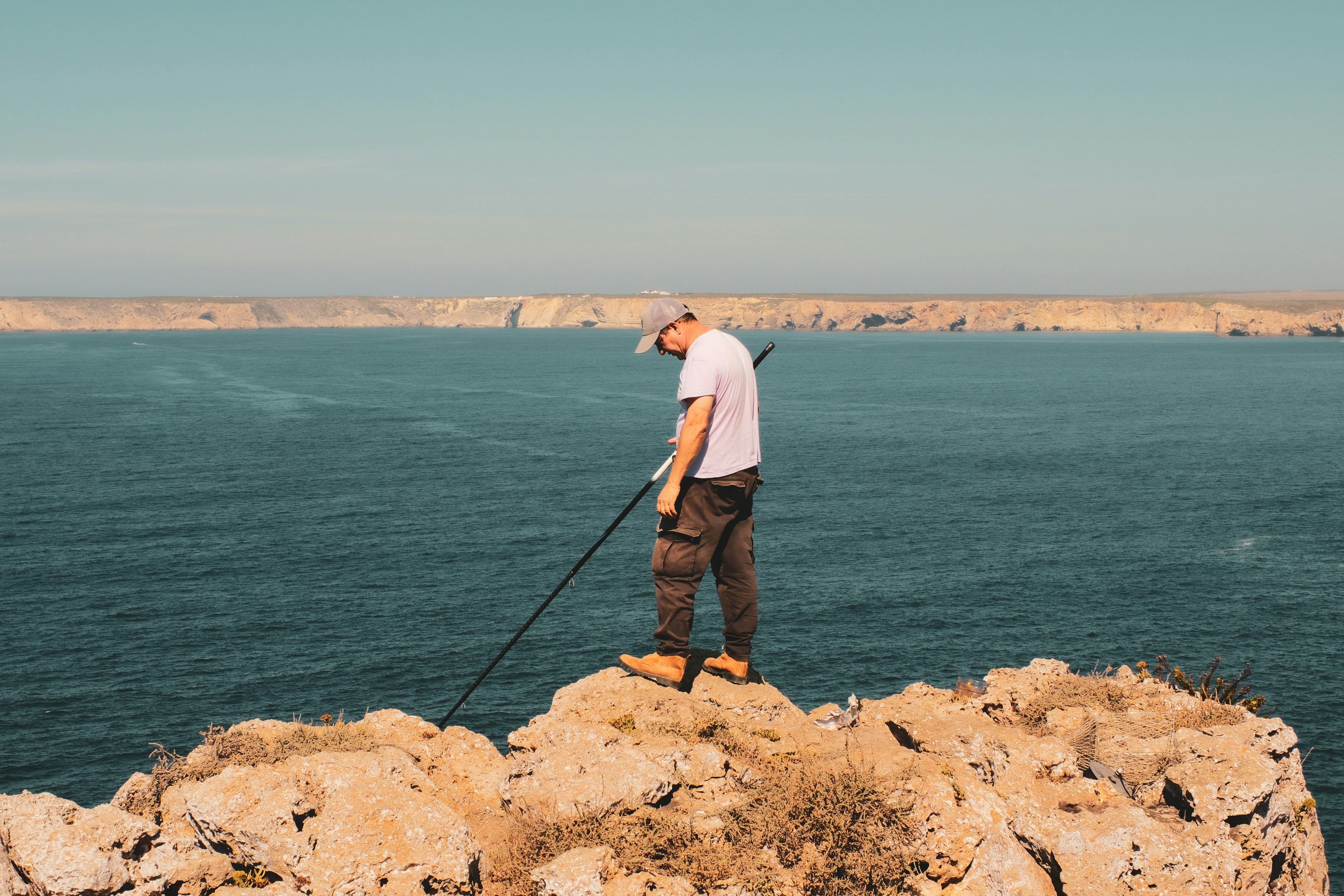 A fisherman standing on the cliffs of Sagres, Algarve, Portugal | Man fishing from a rocky cliff overlooking the ocean