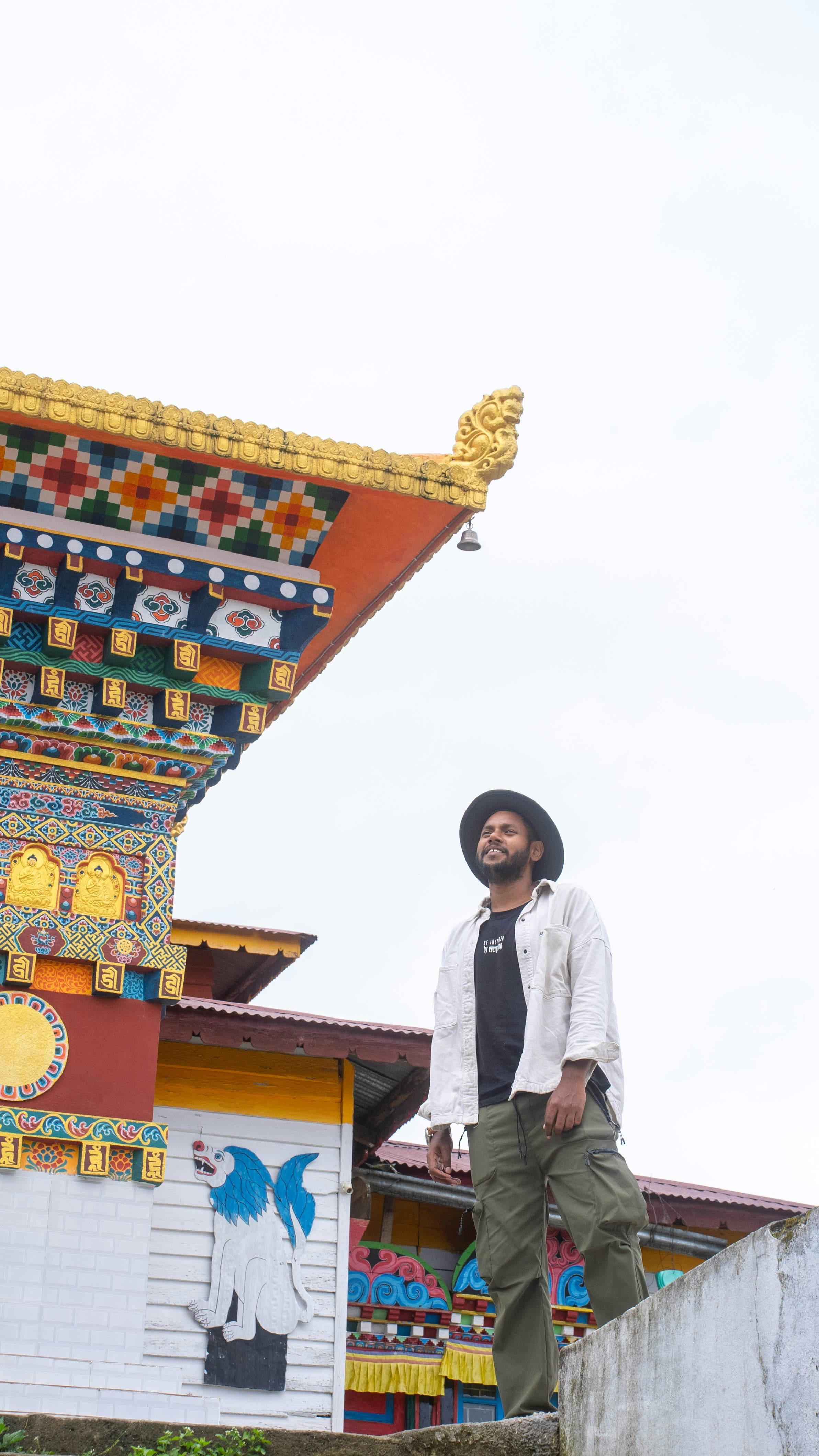 A man stands confidently in front of a vibrant temple adorned with intricate patterns and a striking lion mural. The scene captures the essence of cultural heritage and contemporary life.