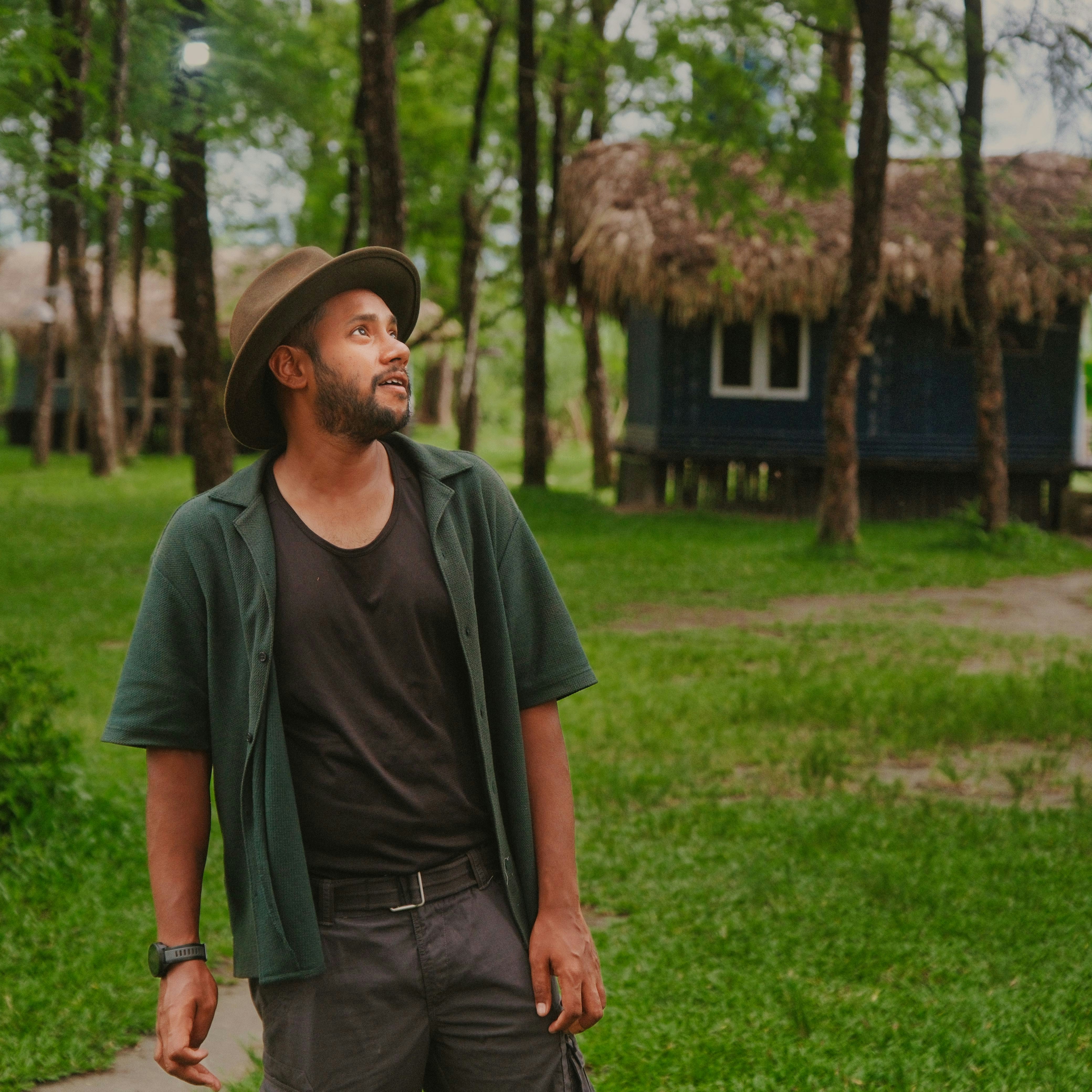 Man gazing upwards amidst lush greenery and rustic huts, embodying a serene connection with nature.