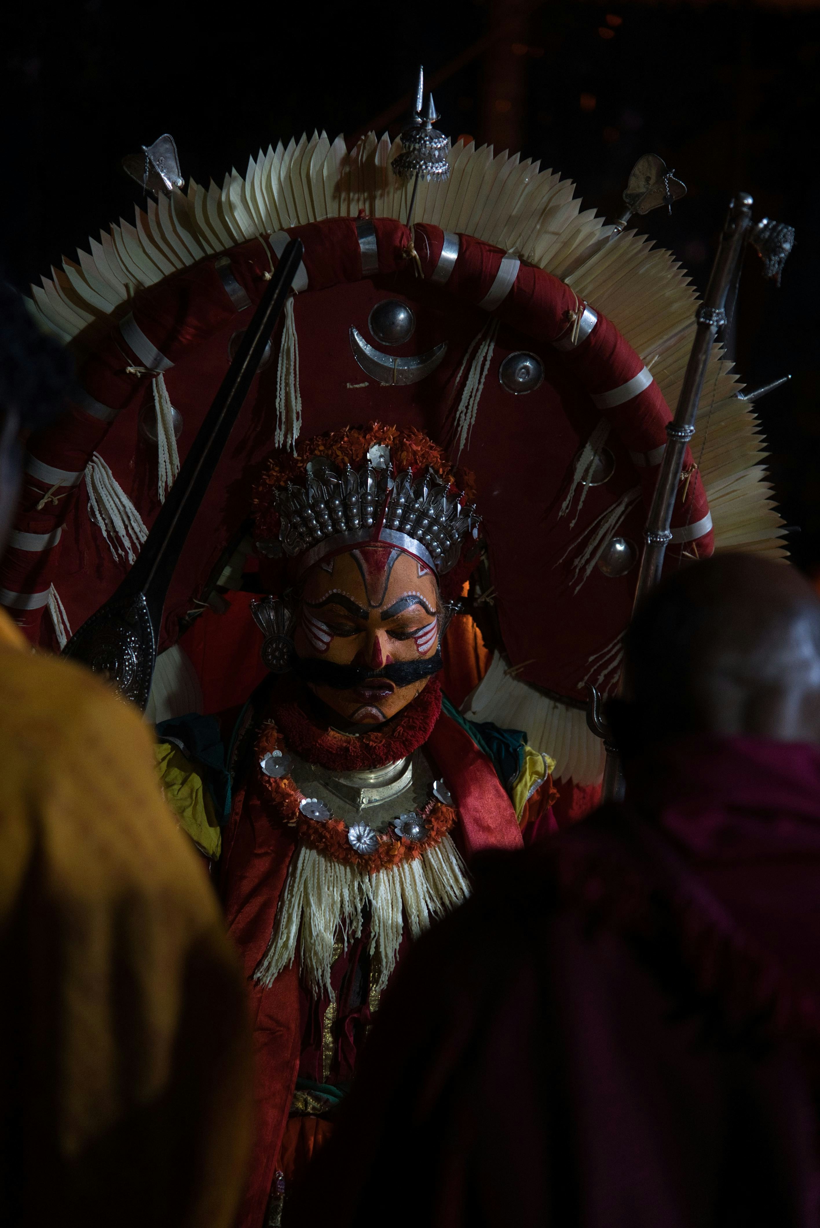 A performer adorned in vibrant costume and intricate makeup, surrounded by spectators during a cultural celebration. The scene captures the essence of traditional artistry and community engagement.