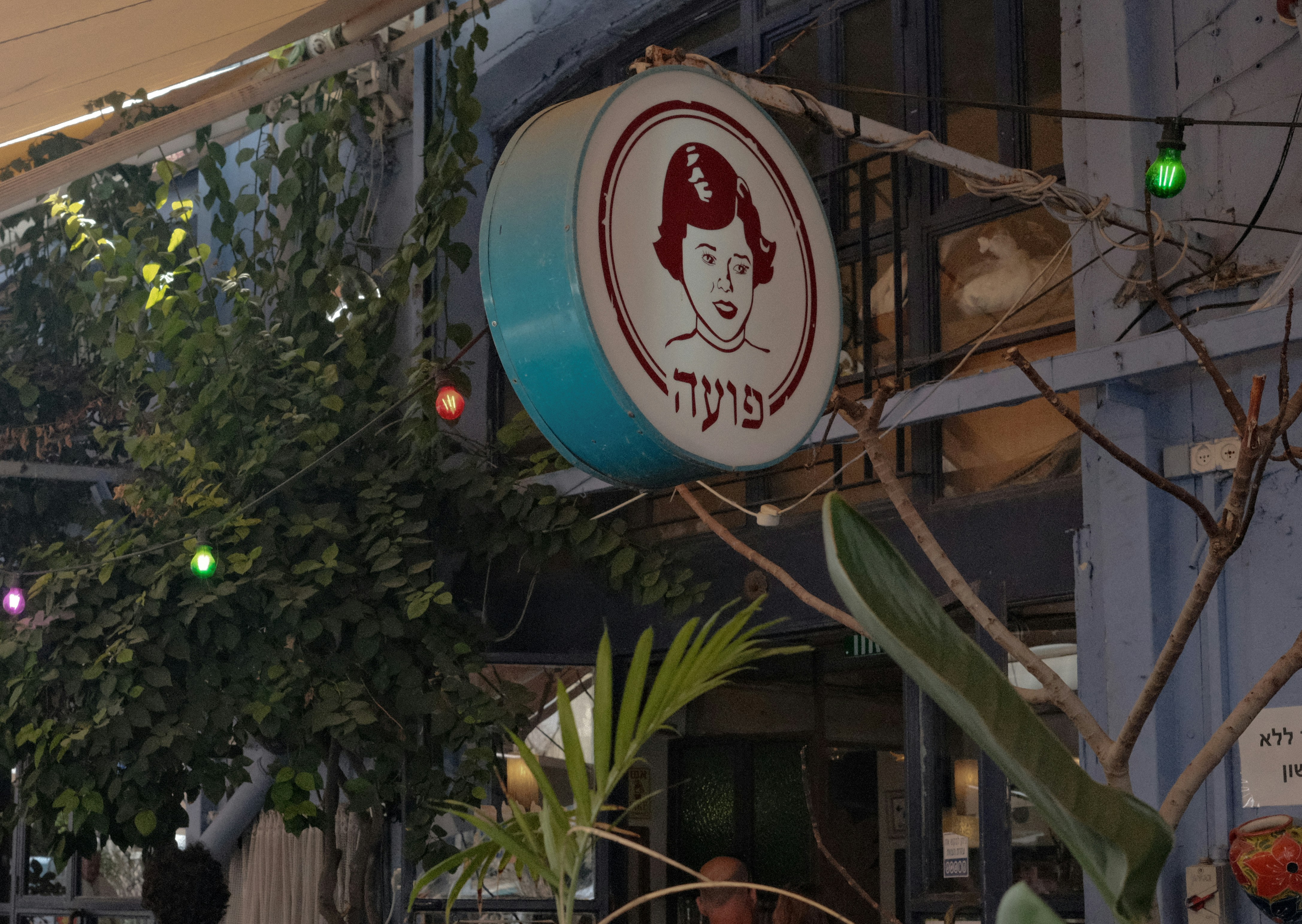 A vibrant restaurant sign featuring a stylized woman’s portrait, surrounded by lush greenery and colorful lights.