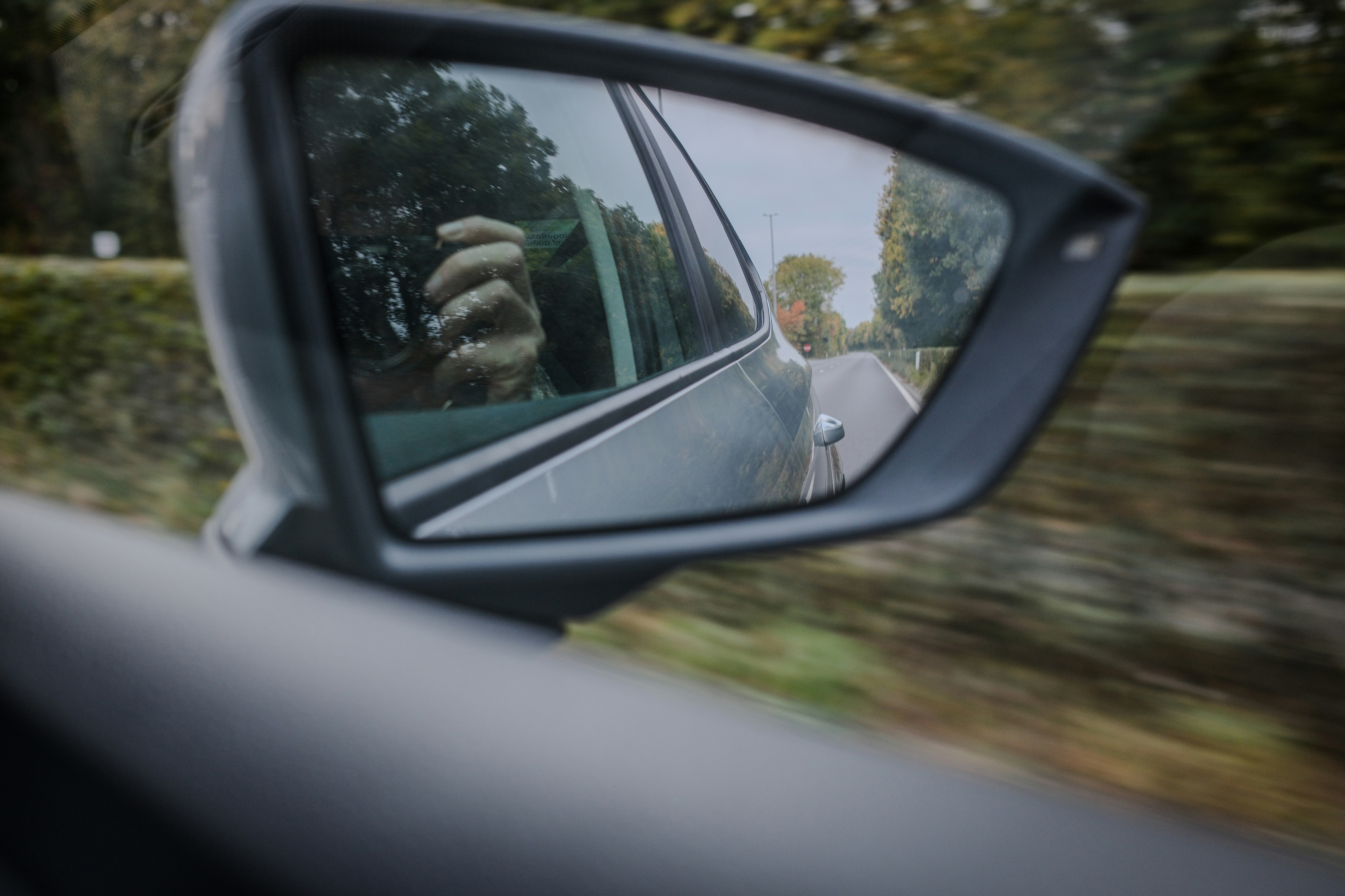 Reflection of hand in car side mirror during drive.