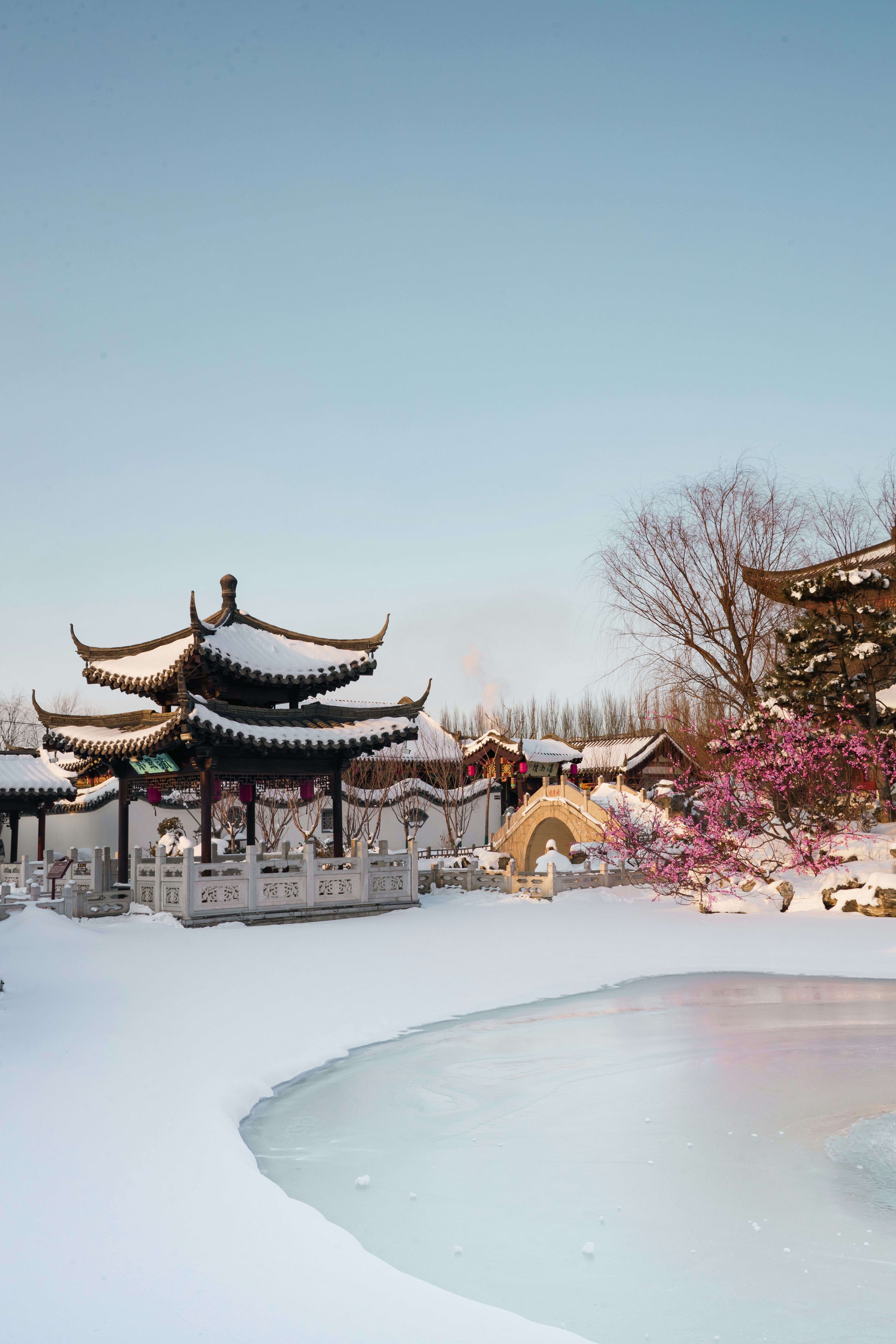Traditional chinese pavilions covered in snow with a frozen pond.