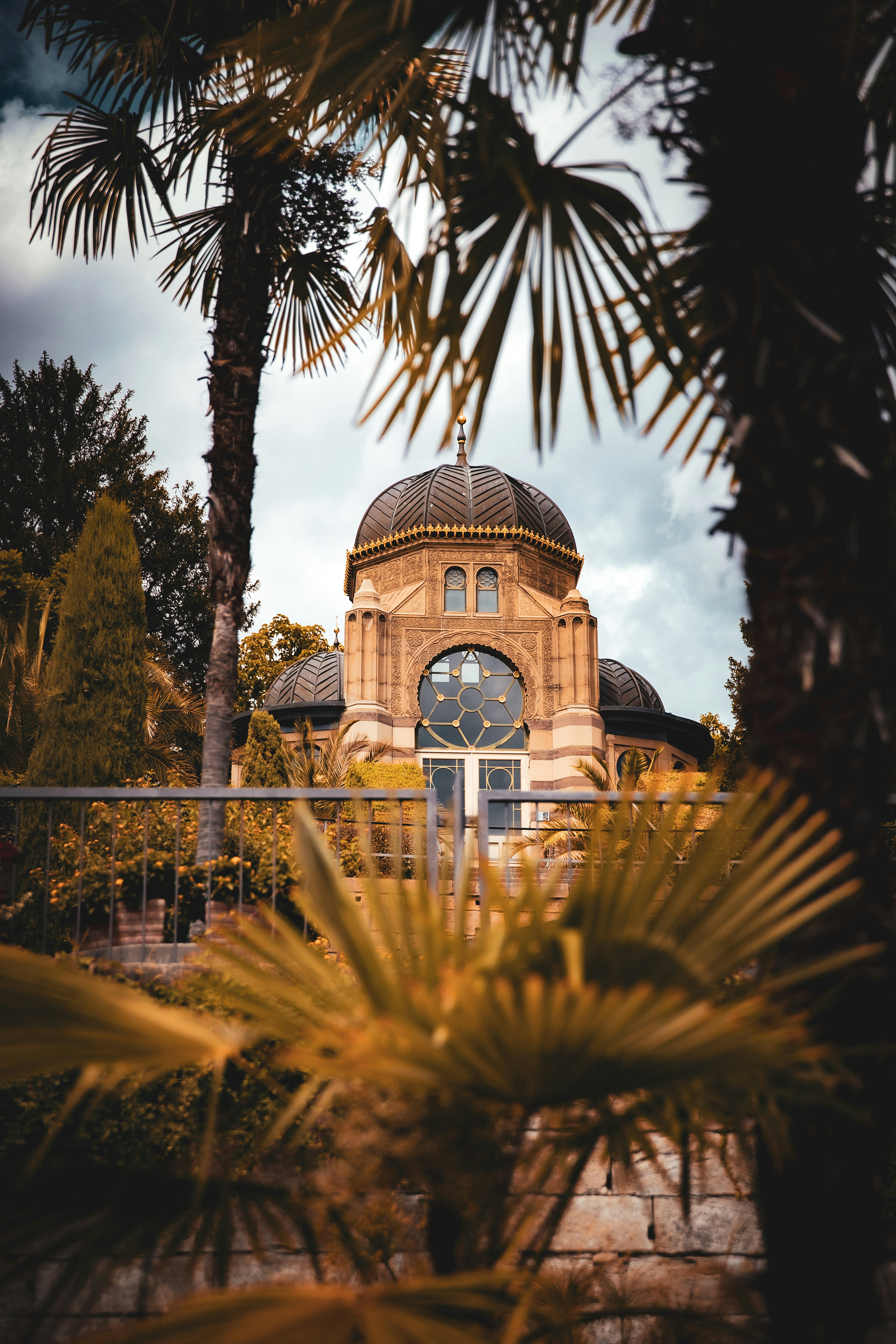 Ornate building framed by tropical foliage, showcasing intricate architectural details and a prominent dome. The scene blends nature with historical elegance.