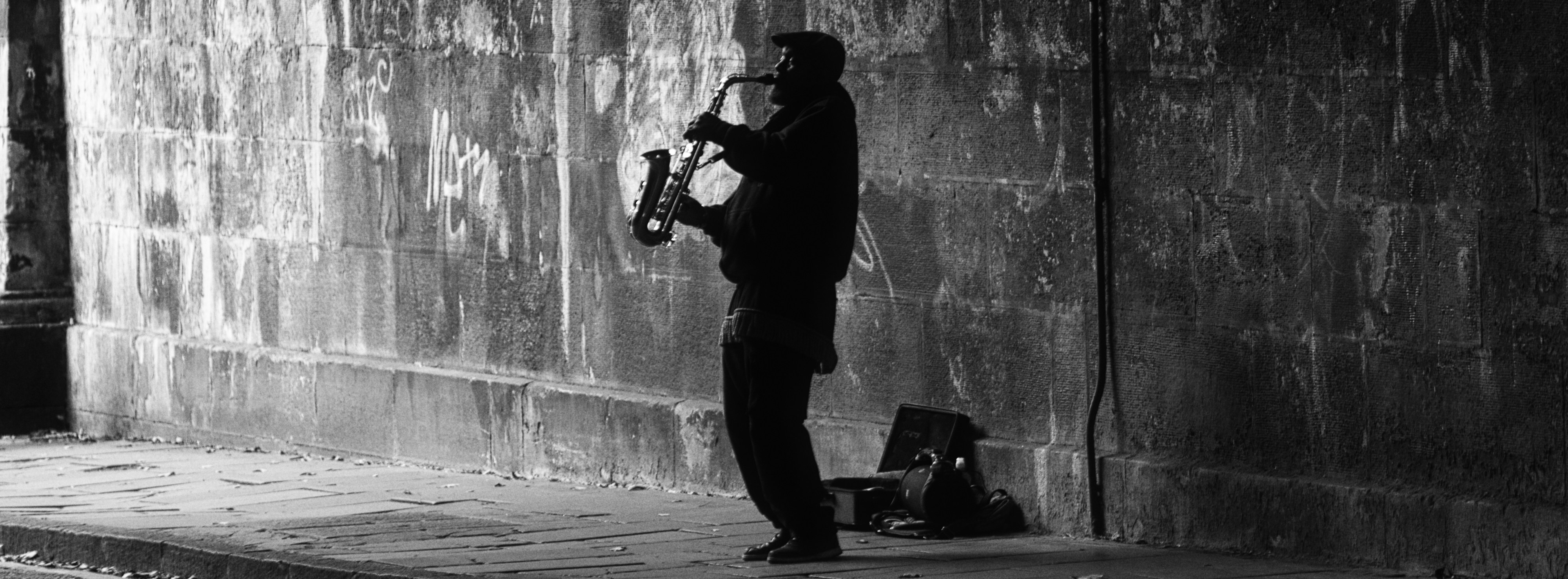 A saxophonist plays against a stone wall in black and white | Man playing saxophone against a textured wall.