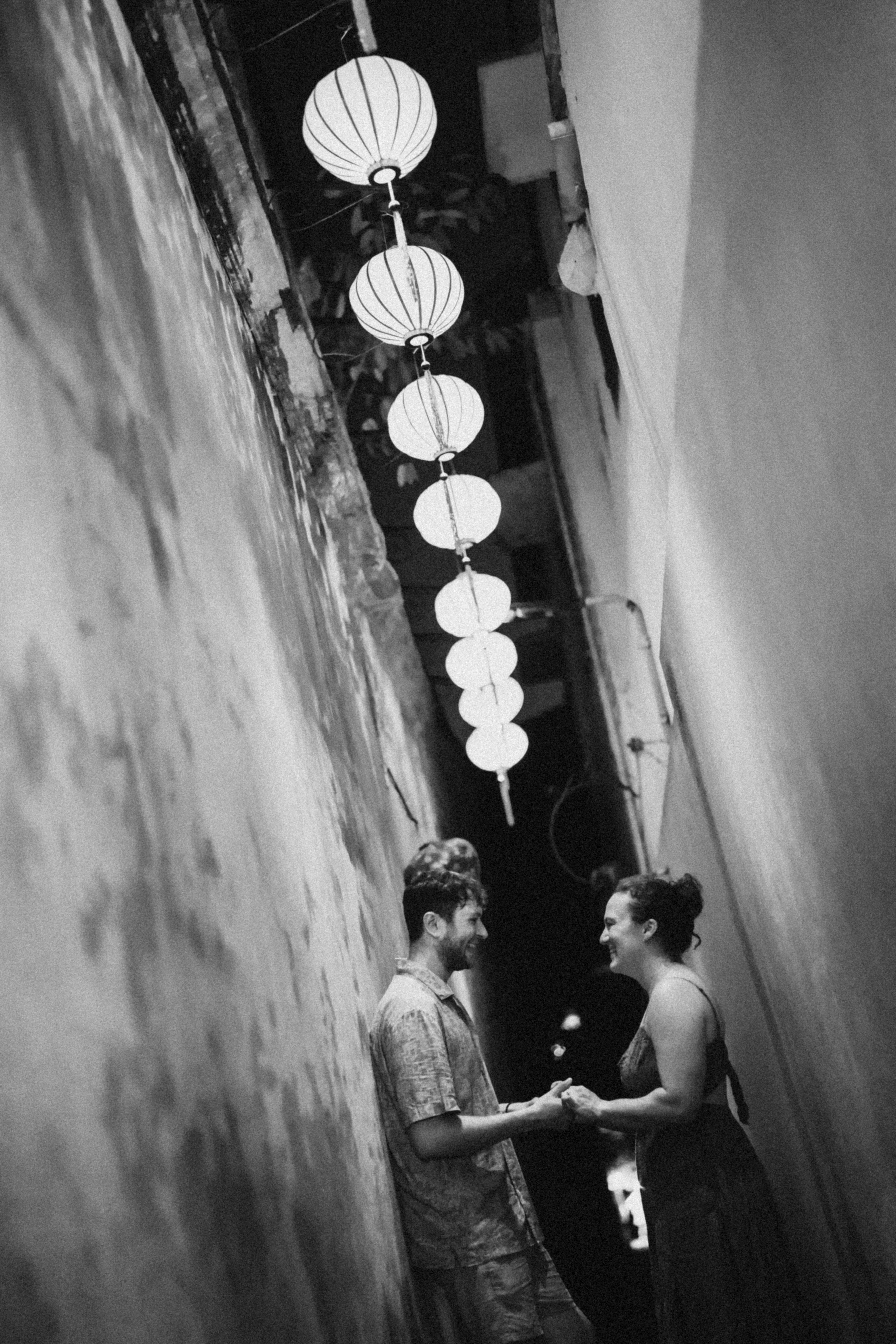 Couple sharing an intimate moment in a narrow alley illuminated by hanging lanterns.