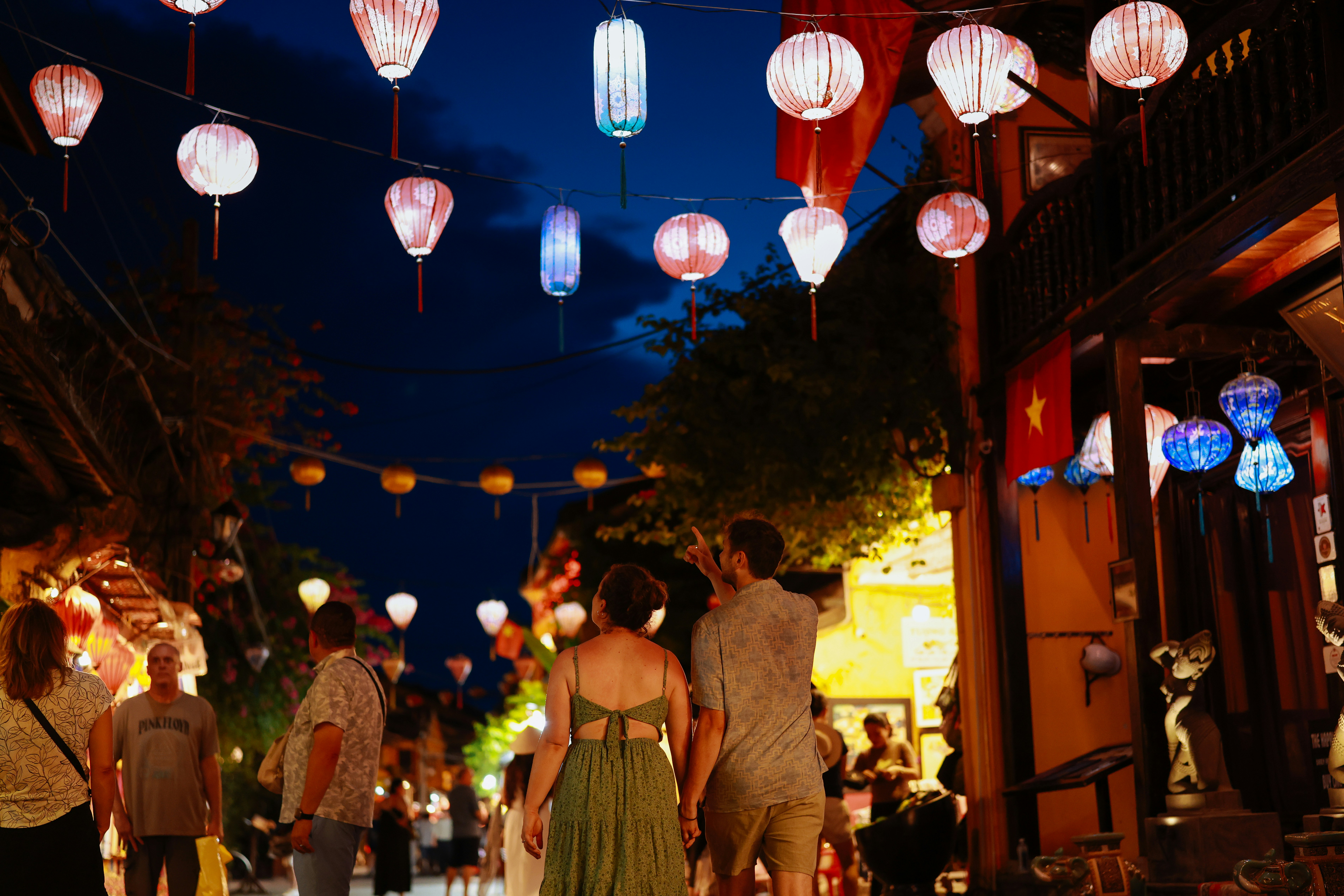 Couple walking hand-in-hand down a vibrant street adorned with colorful lanterns at dusk.