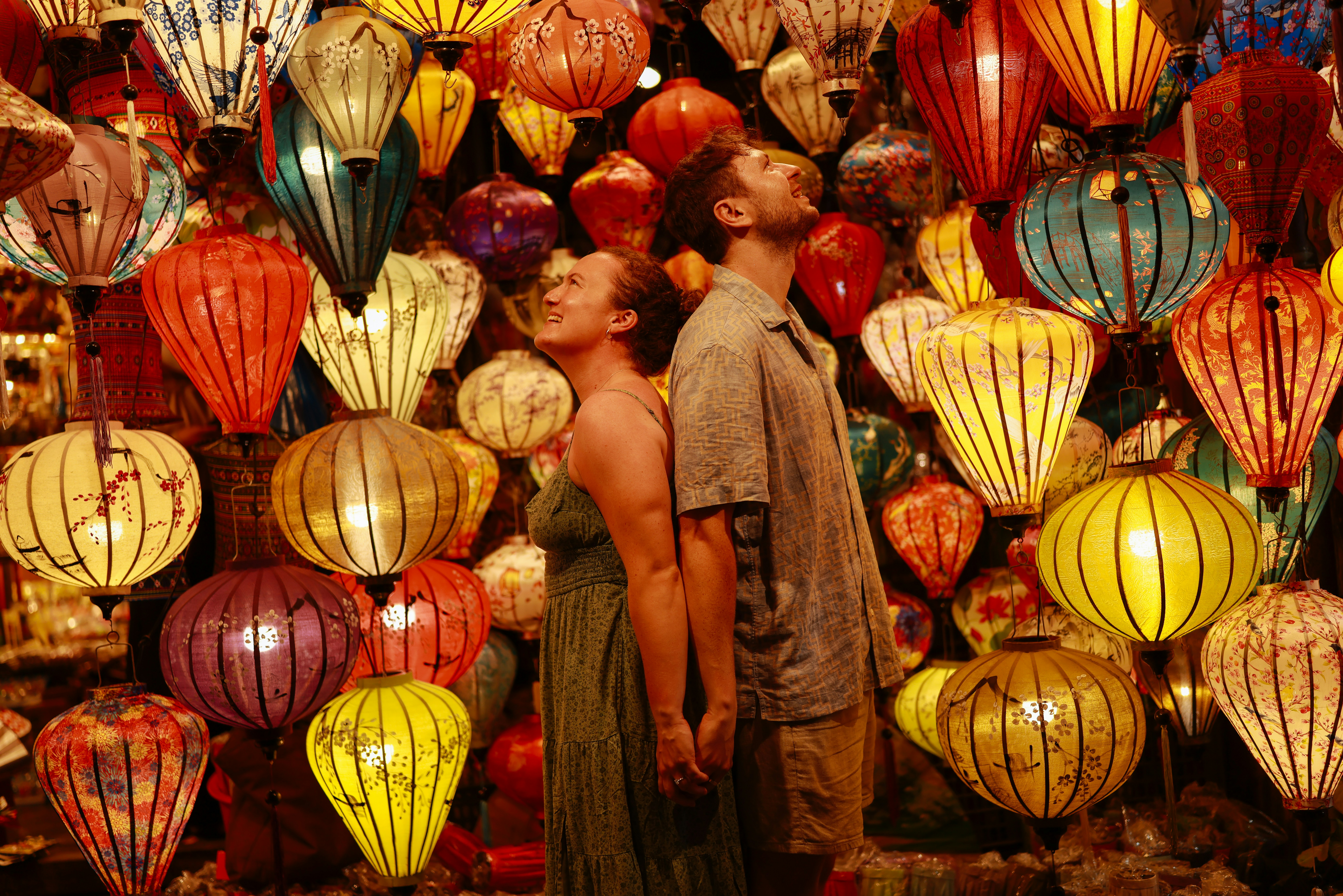 Couple standing back-to-back among a vibrant display of colorful lanterns, creating a whimsical atmosphere filled with warmth and light.