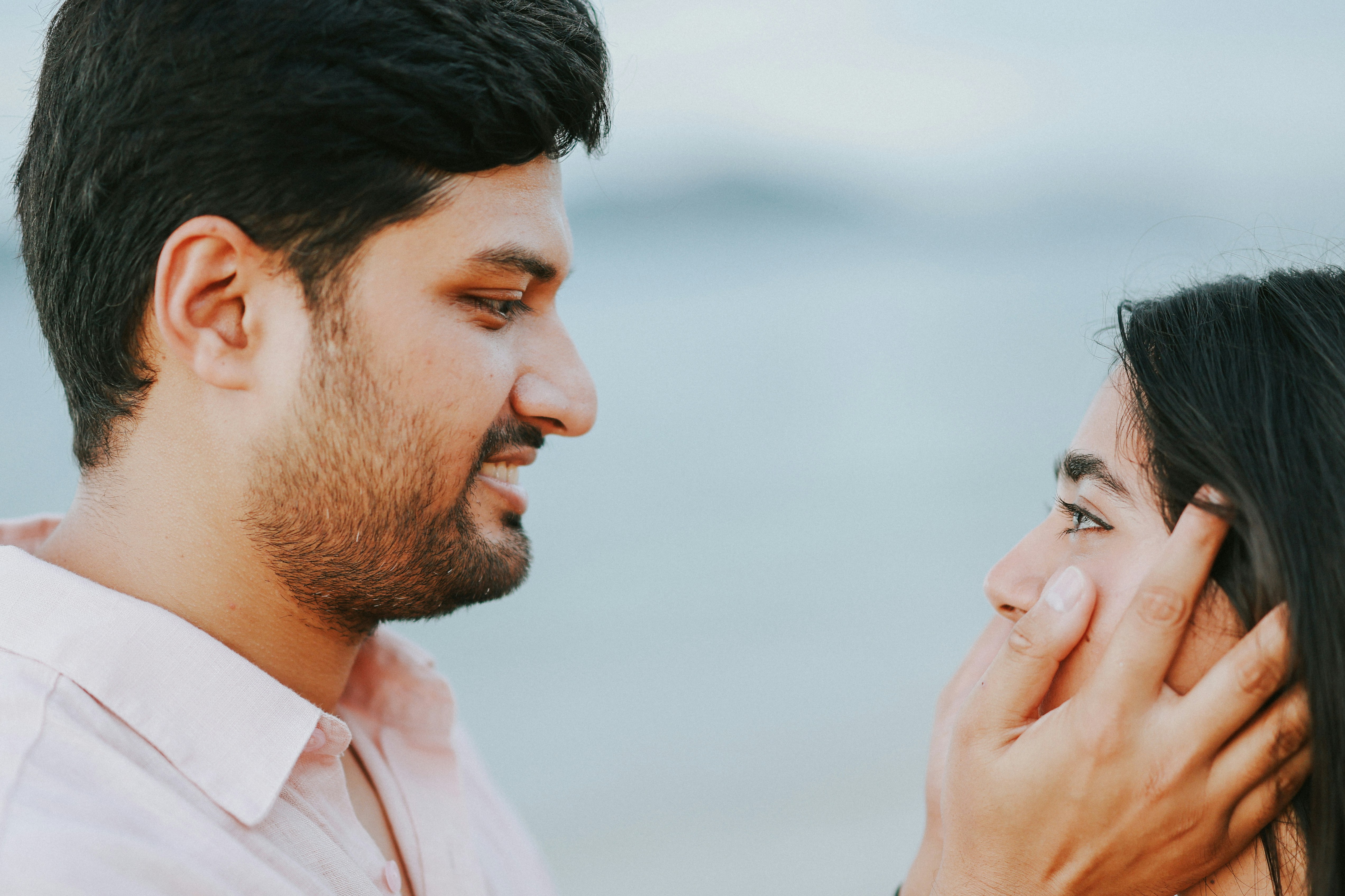 Two individuals sharing an intimate moment on a beach, with soft expressions and gentle gestures. The serene background enhances the emotional connection.
