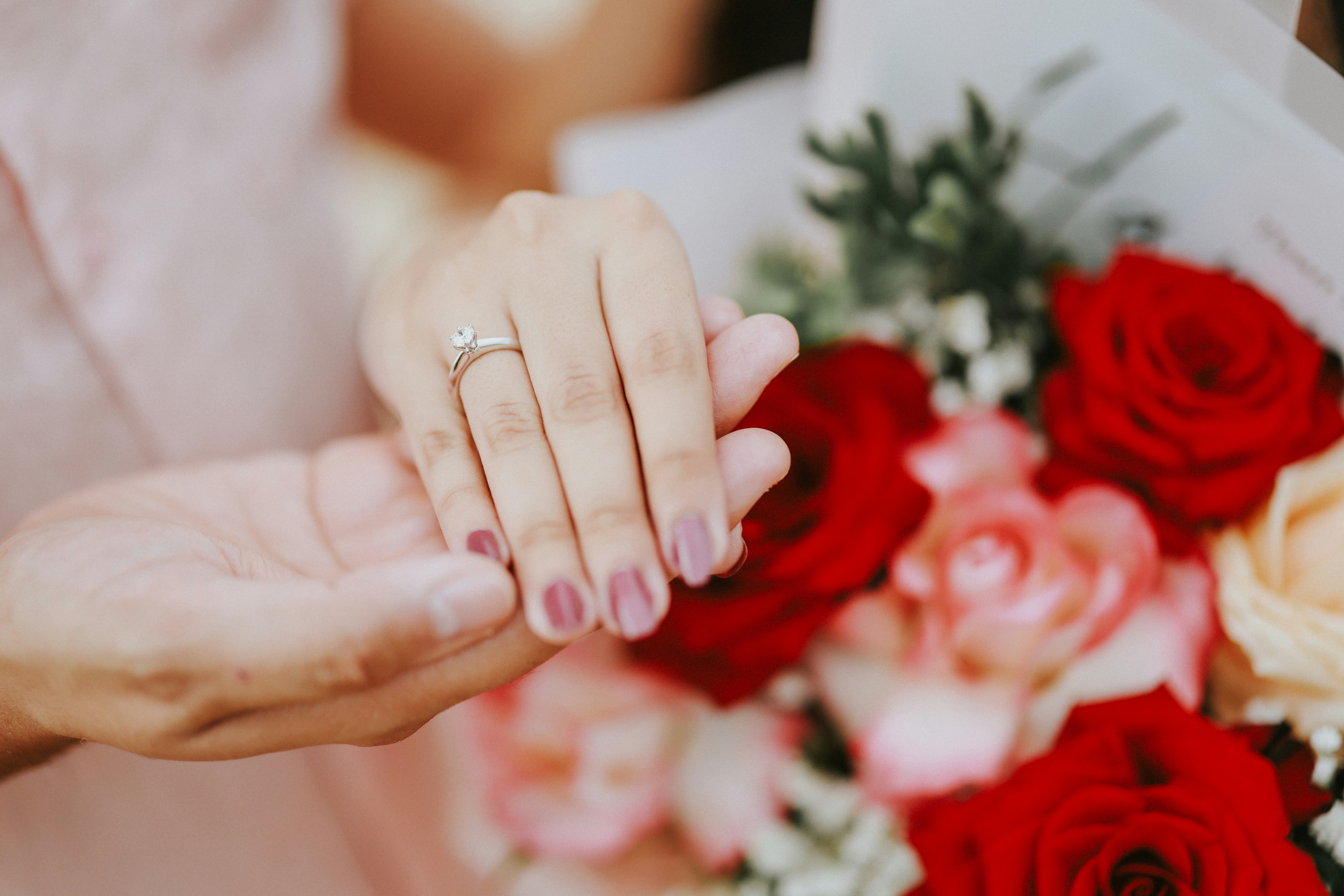 Couple holding hands with engagement ring and roses