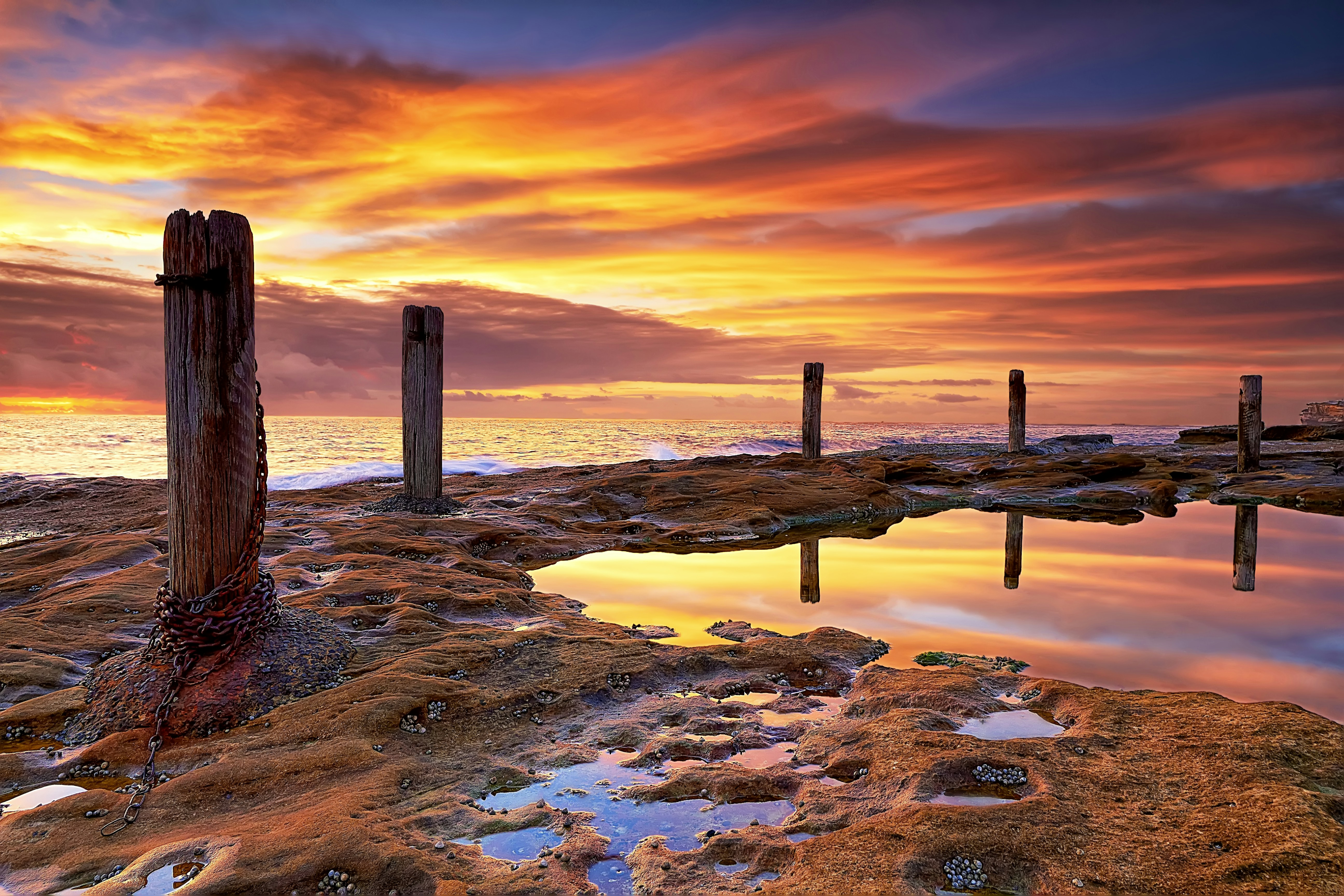 Wooden posts on rocky shore at sunset