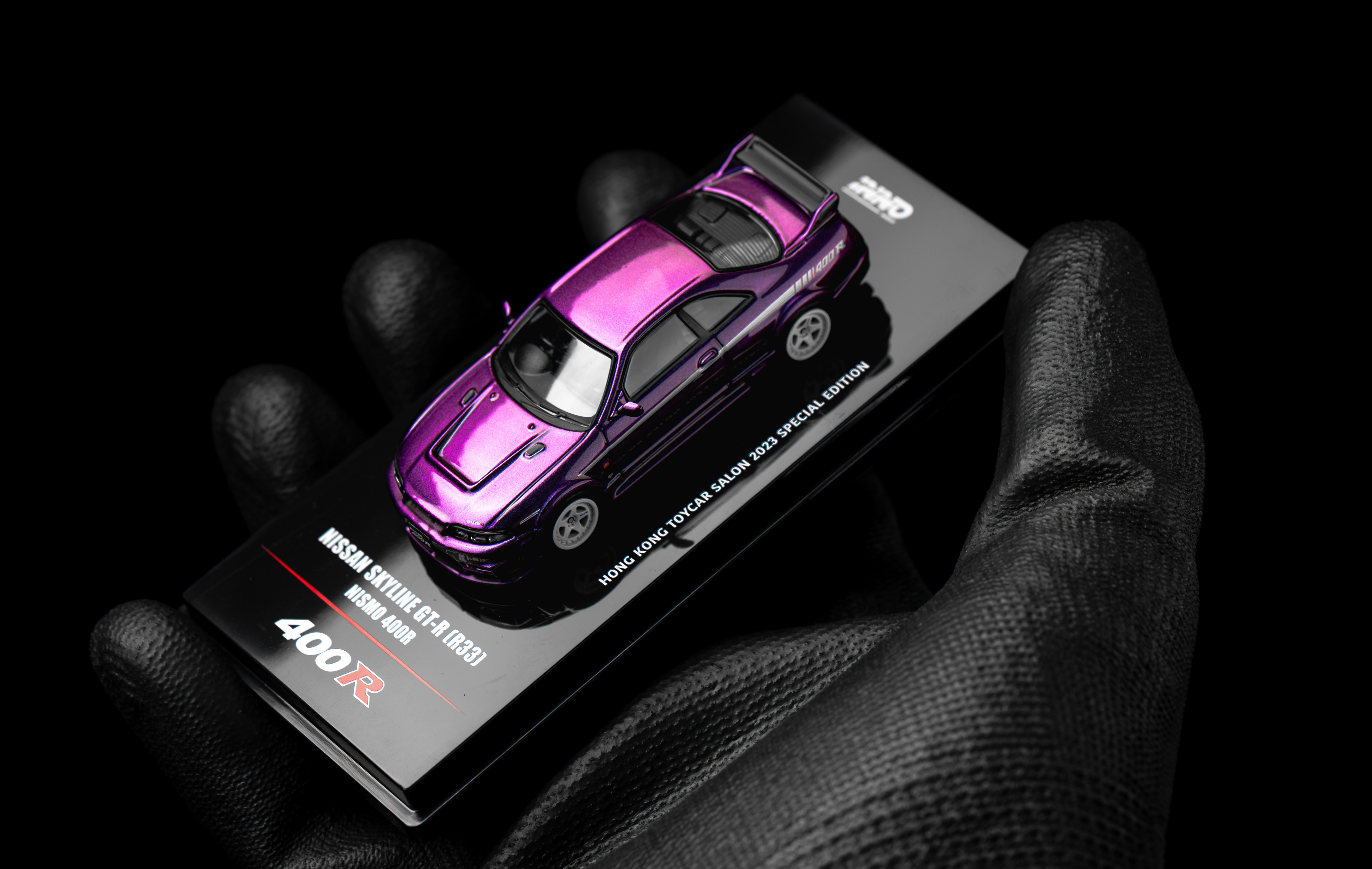 Hand holding a purple model car on a black base.
