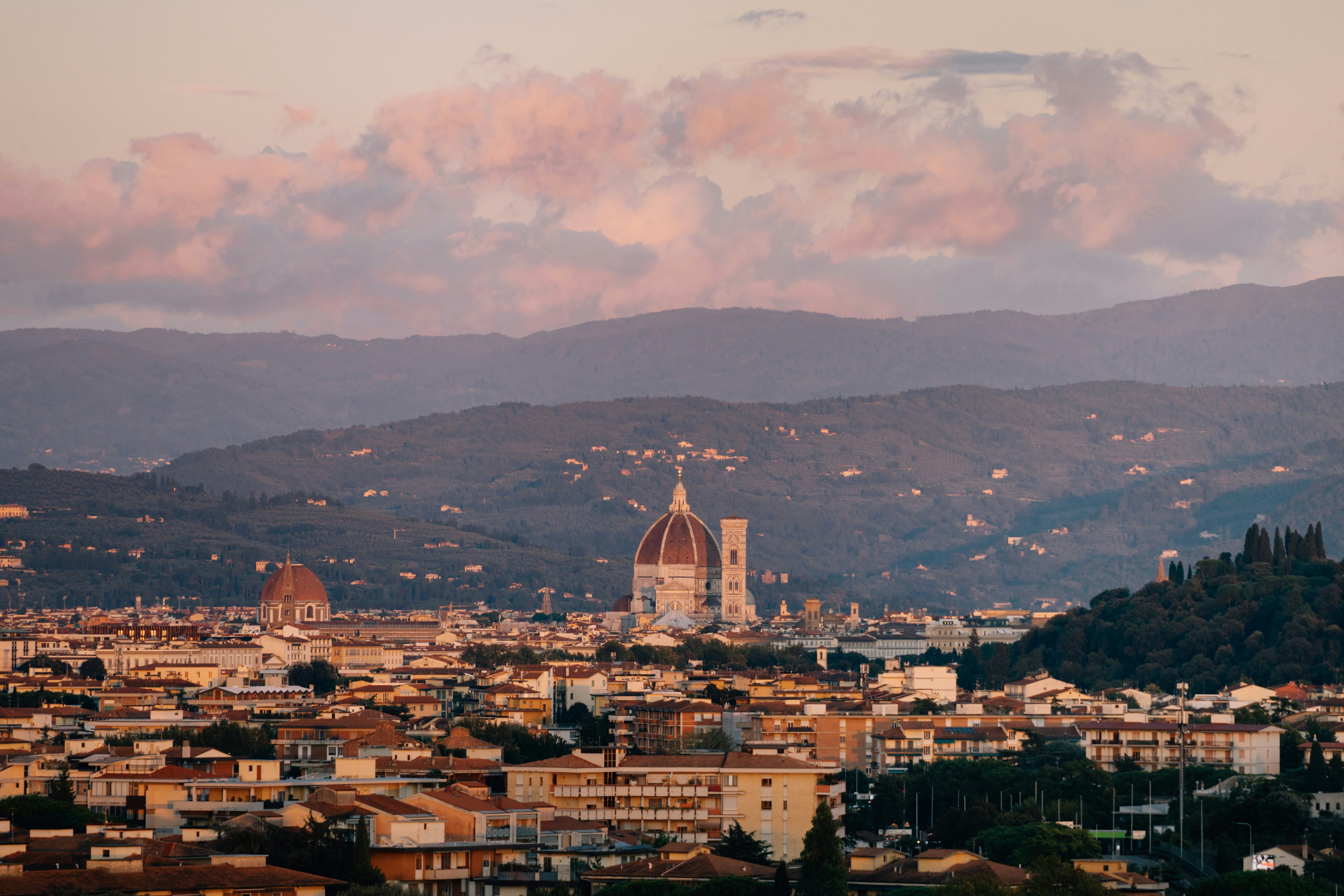 Panoramic view of Florence showcasing the iconic Duomo and bell tower against a backdrop of rolling hills and pastel clouds.
