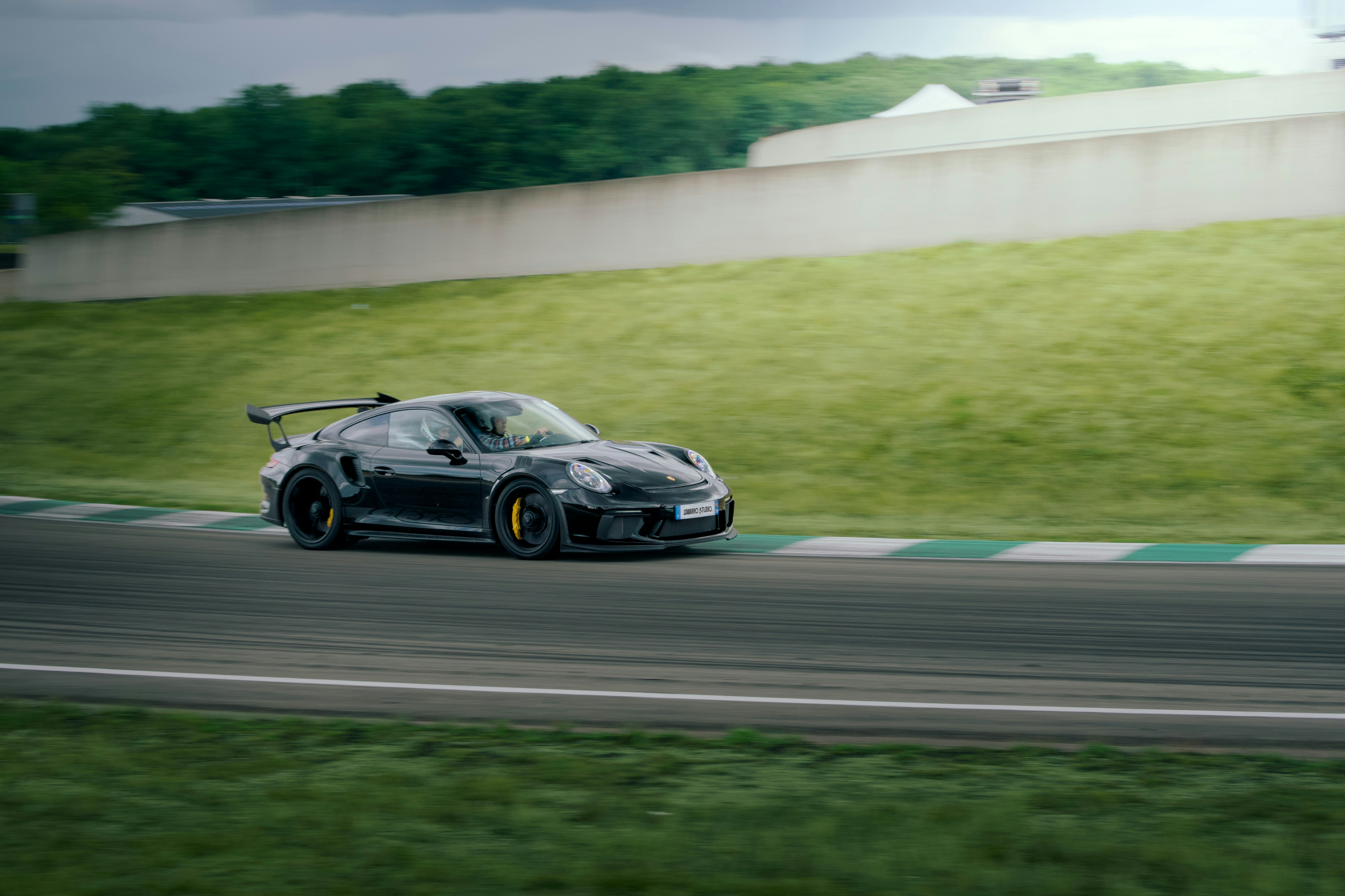 A sleek black sports car races around a track, showcasing its aerodynamic design against a blurred green landscape.
