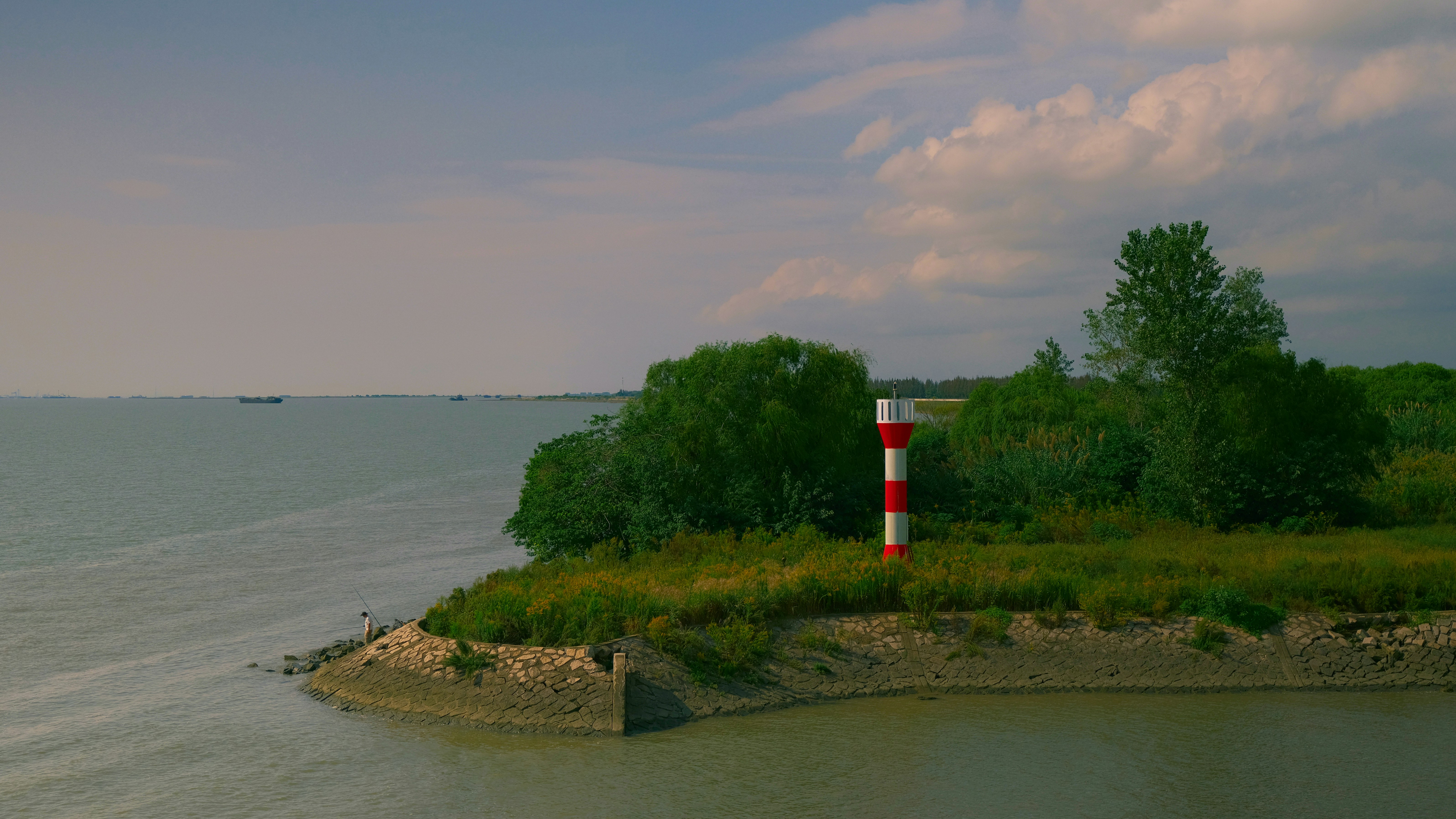 Red and white striped marker on grassy island near water.