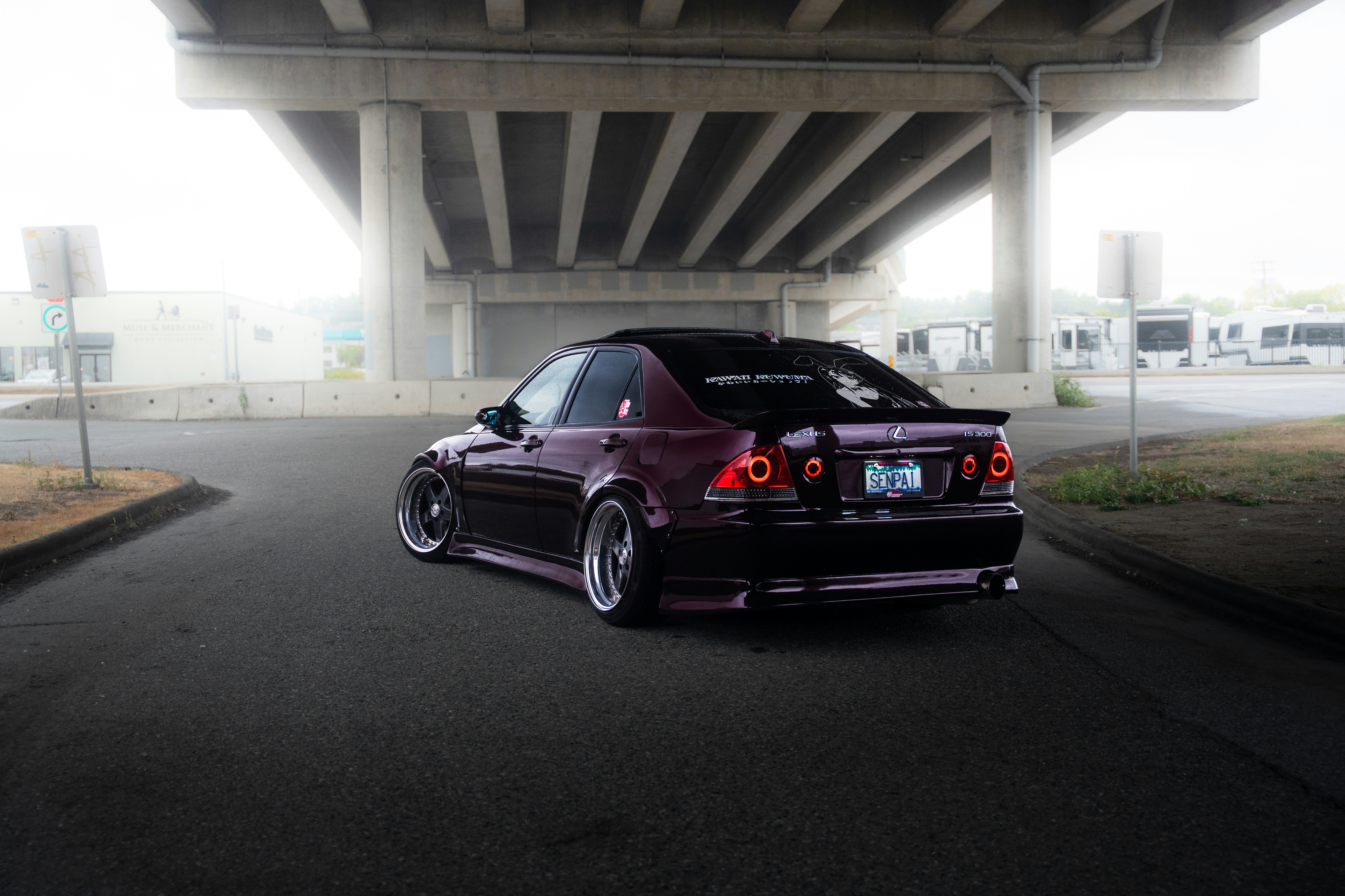 Modified sedan parked in an urban setting, showcasing sleek lines and unique styling against a backdrop of concrete structures.