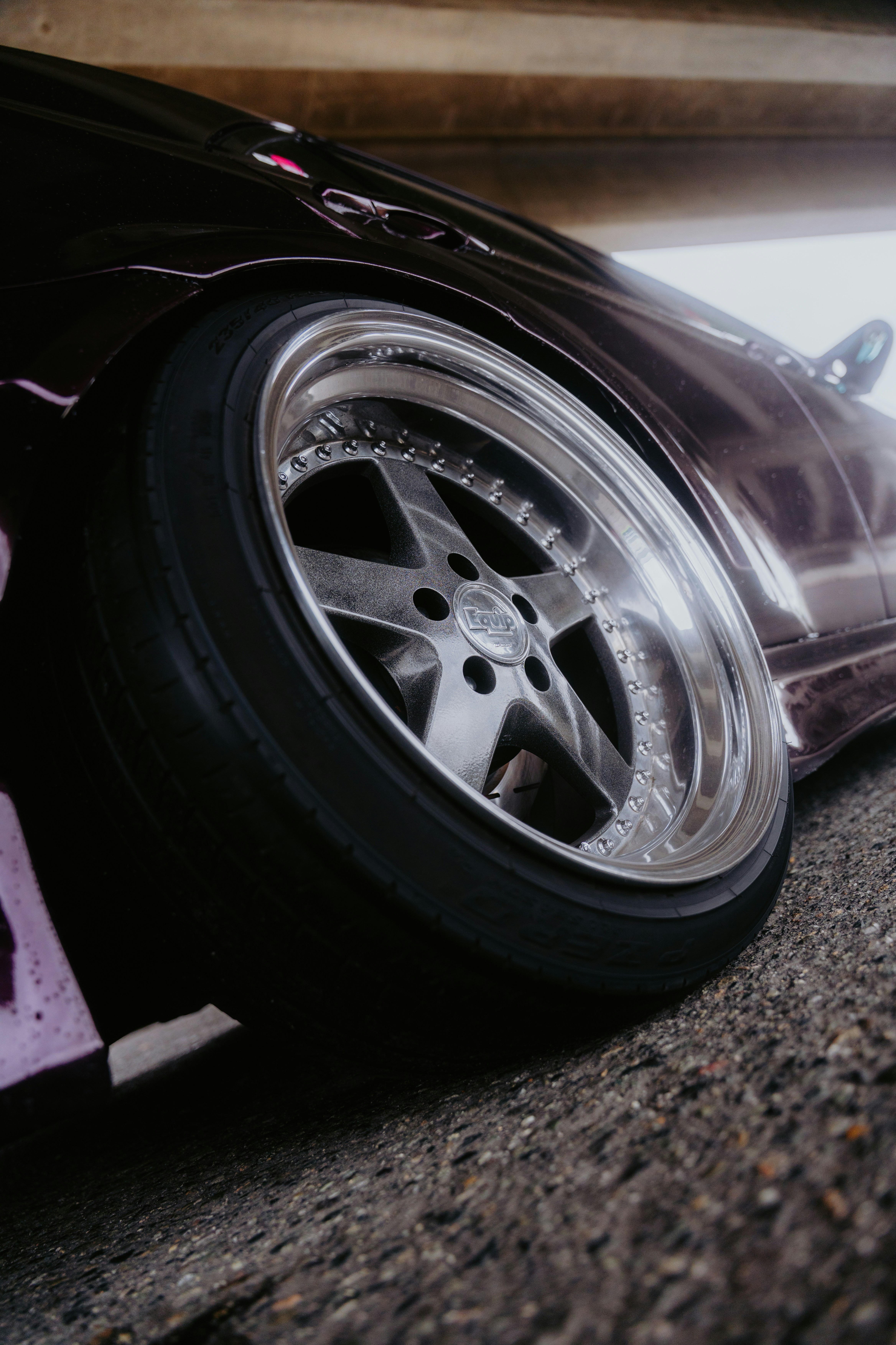 Close-up view of a custom alloy wheel and tire, showcasing intricate design and craftsmanship under a concrete structure.